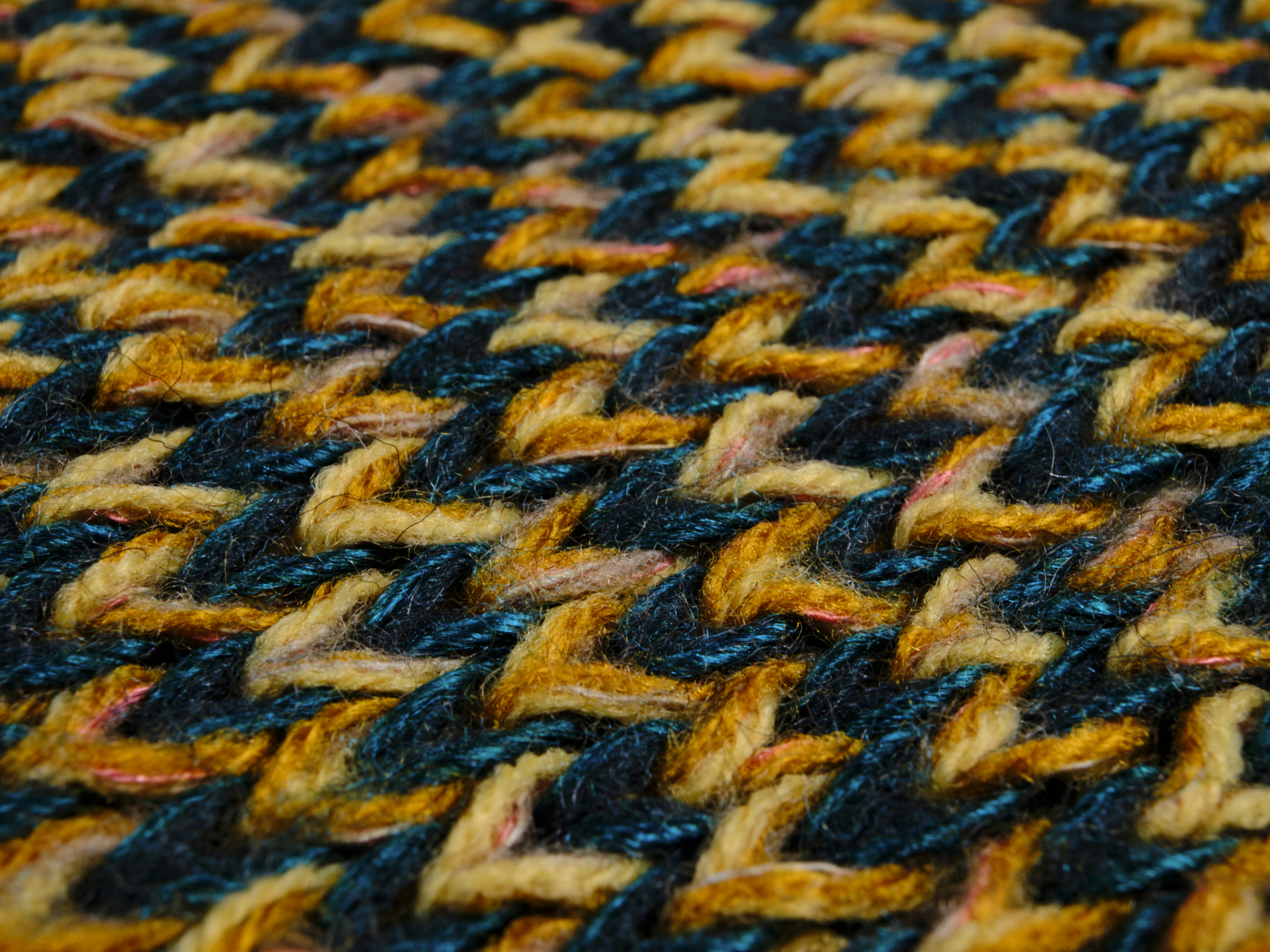 Close-up of a woven textile featuring intricate patterns in warm hues of gold, black, and blue. The craftsmanship showcases the tactile quality of the fabric.