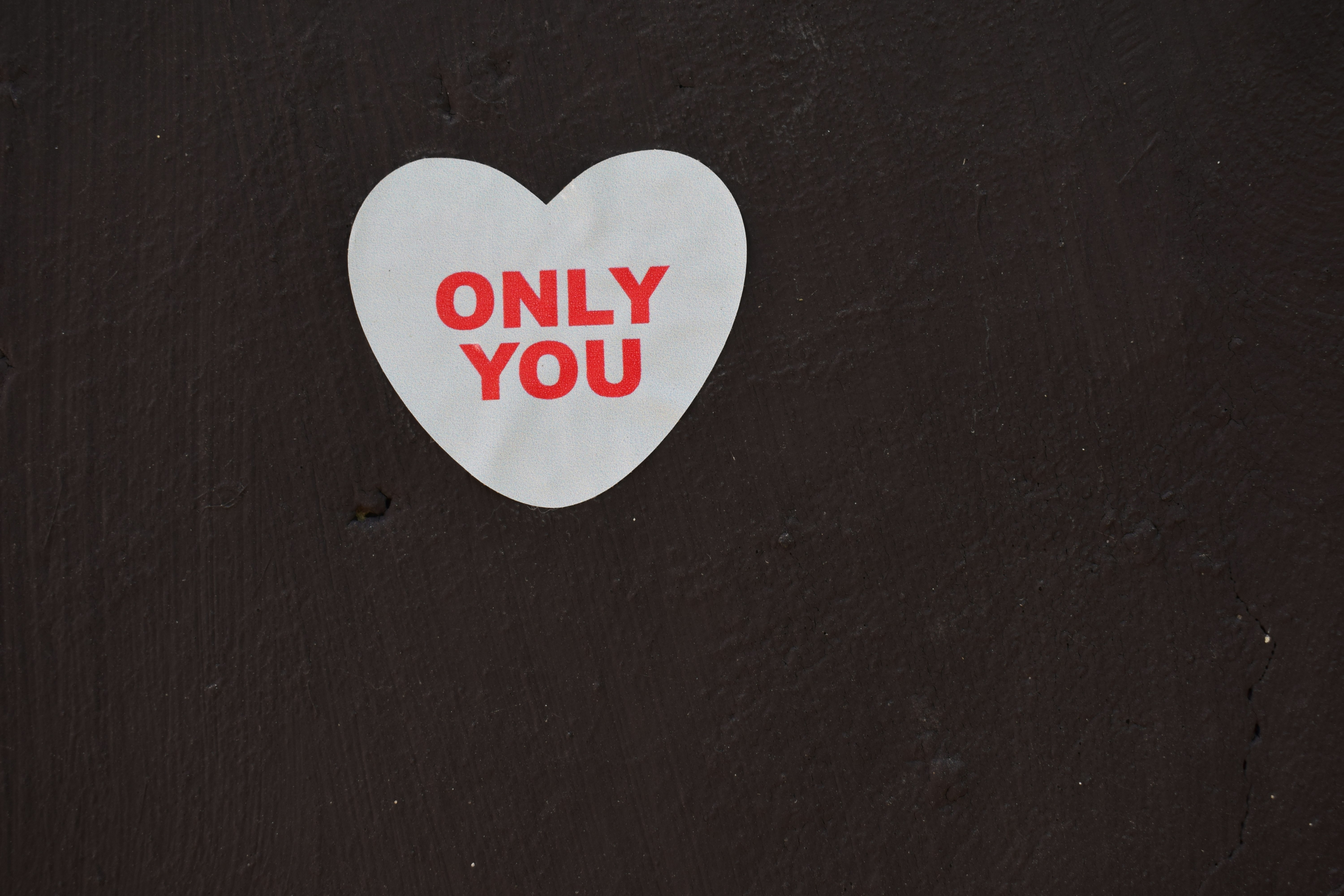 Heart-shaped sticker with bold red text reading 'ONLY YOU' affixed to a textured dark surface.