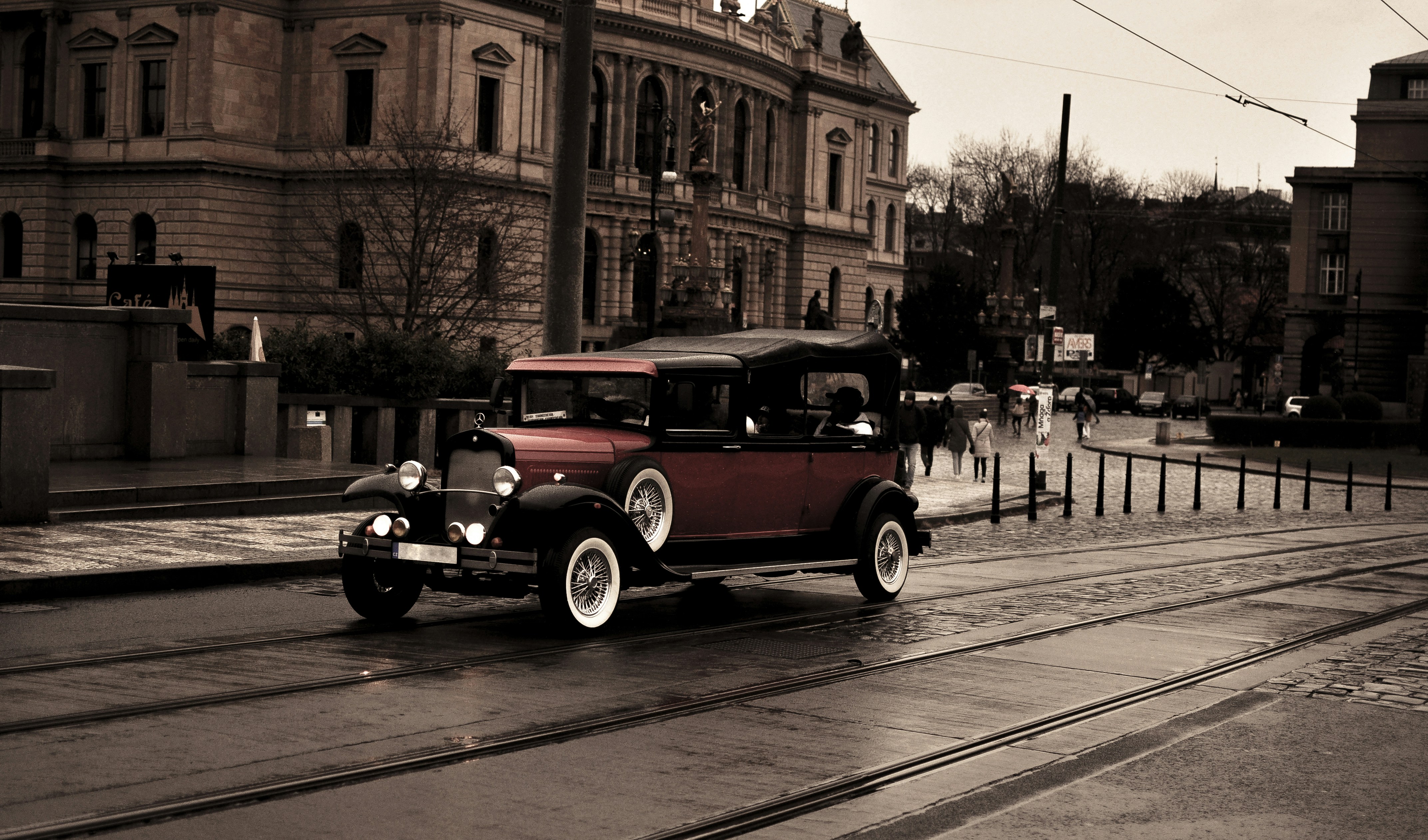 Vintage car cruising along wet city streets, surrounded by historic architecture and a moody atmosphere.