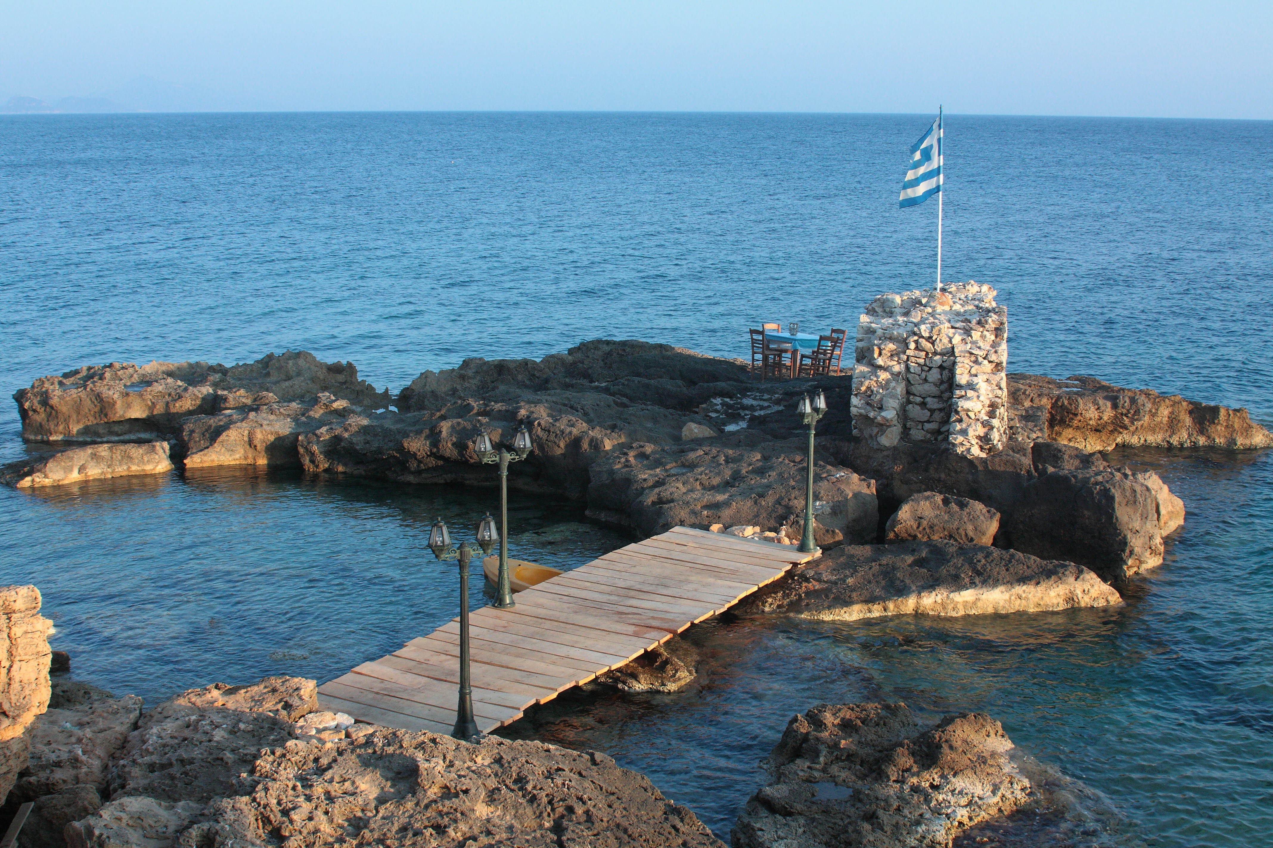 Edge of Quiet Blue: The Greek Flag Over a Stone Pier