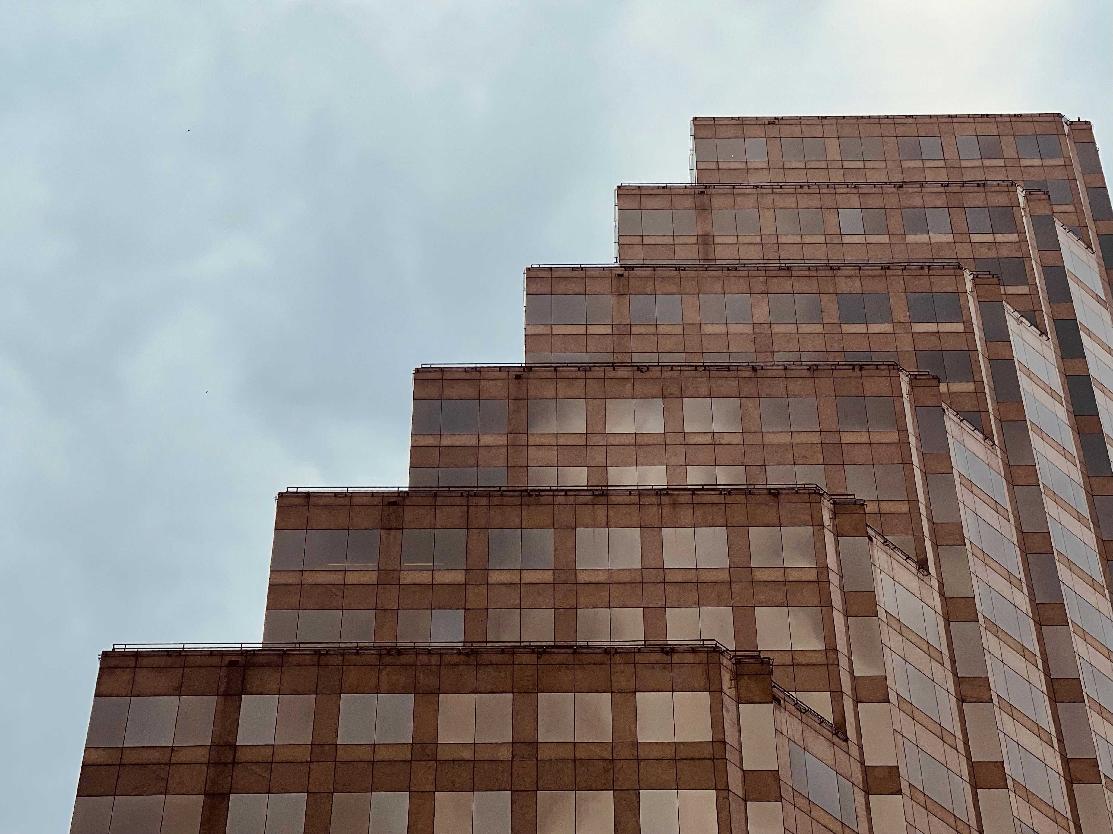 Tiered architectural structure with reflective windows against a cloudy sky.