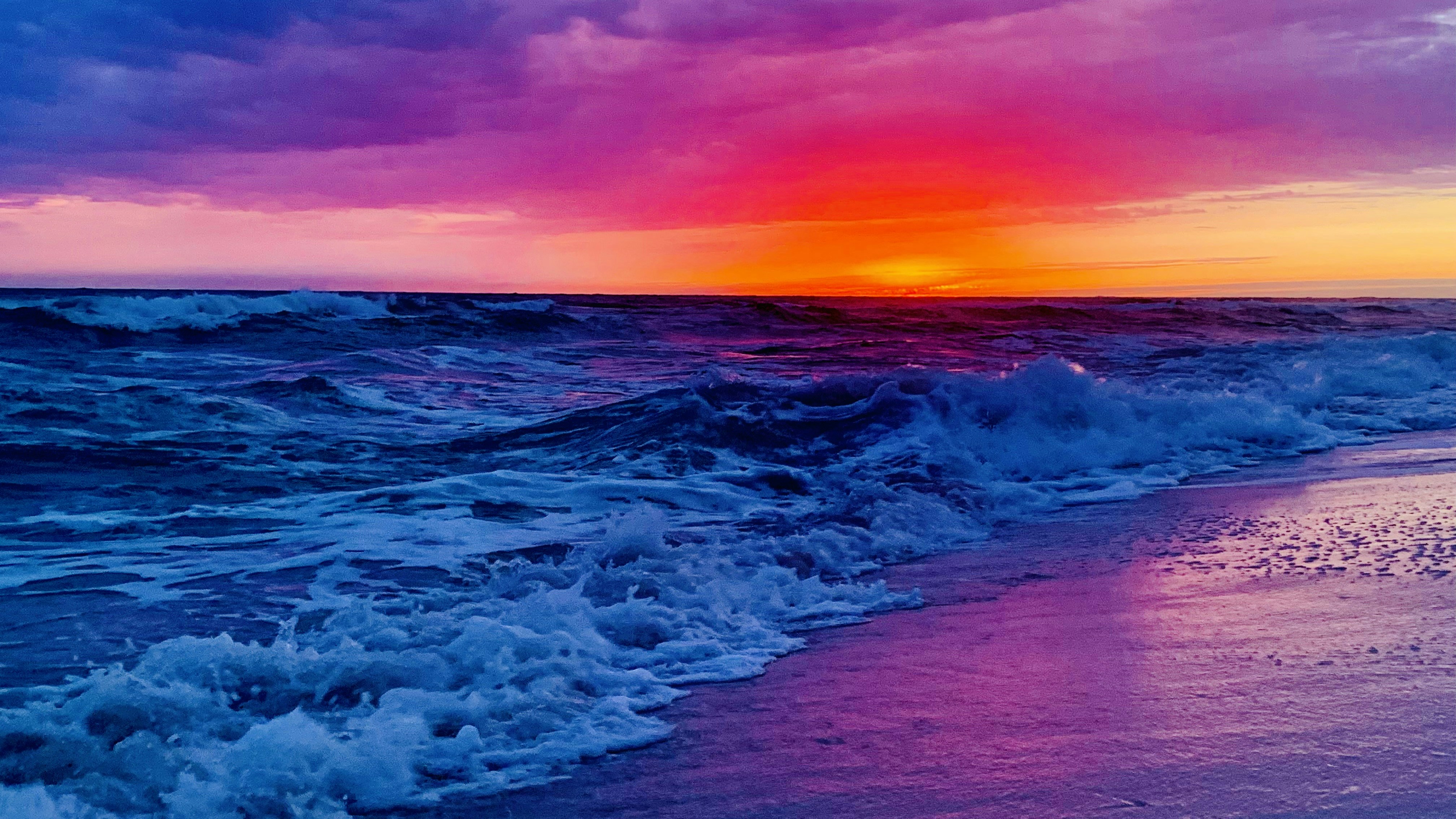 Vibrant sunset reflecting on ocean waves, with a gradient of purple and orange hues illuminating the sky. The scene captures the tranquil beauty of twilight by the shore.