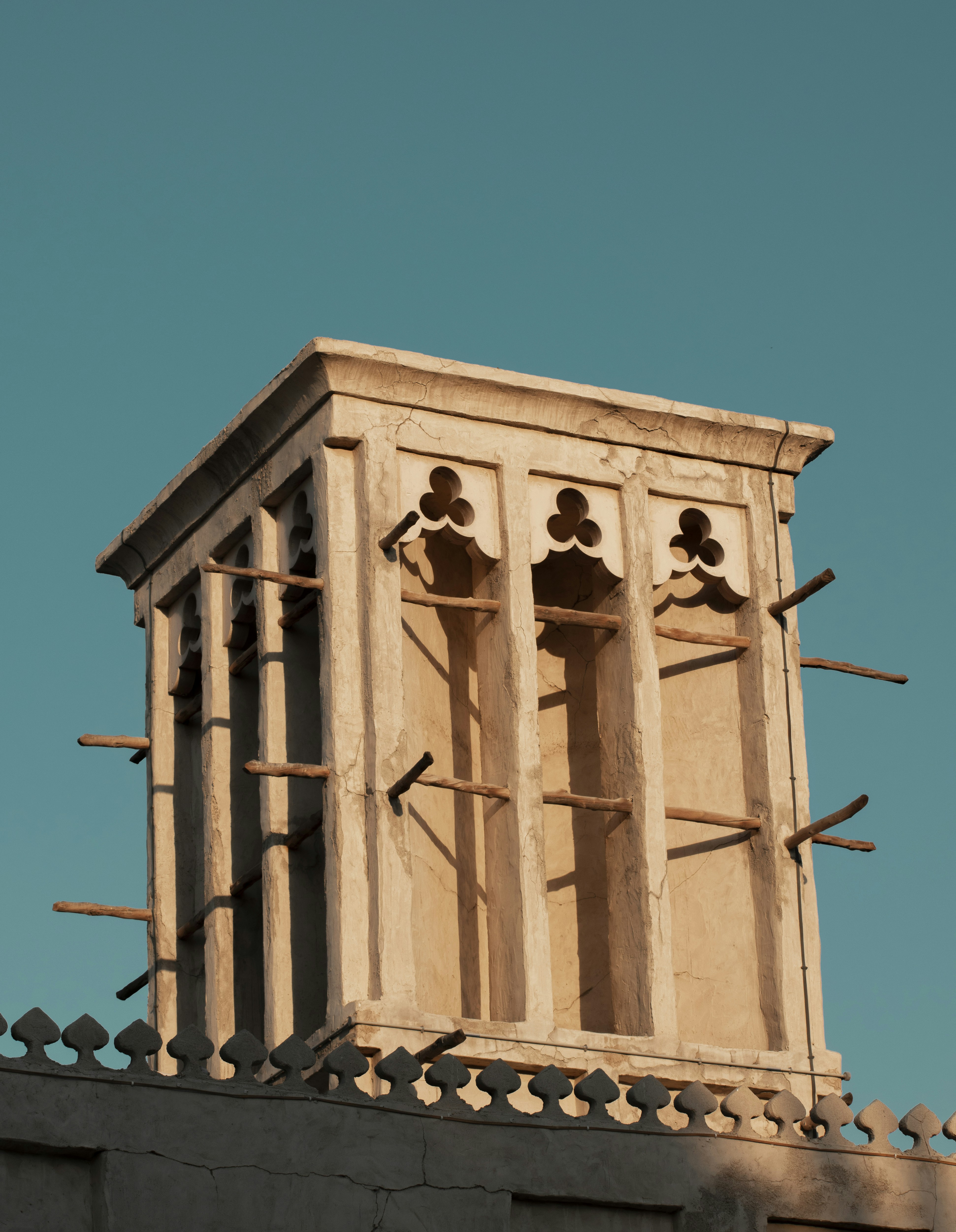 Historic wind tower rising above a traditional structure against a clear blue sky.