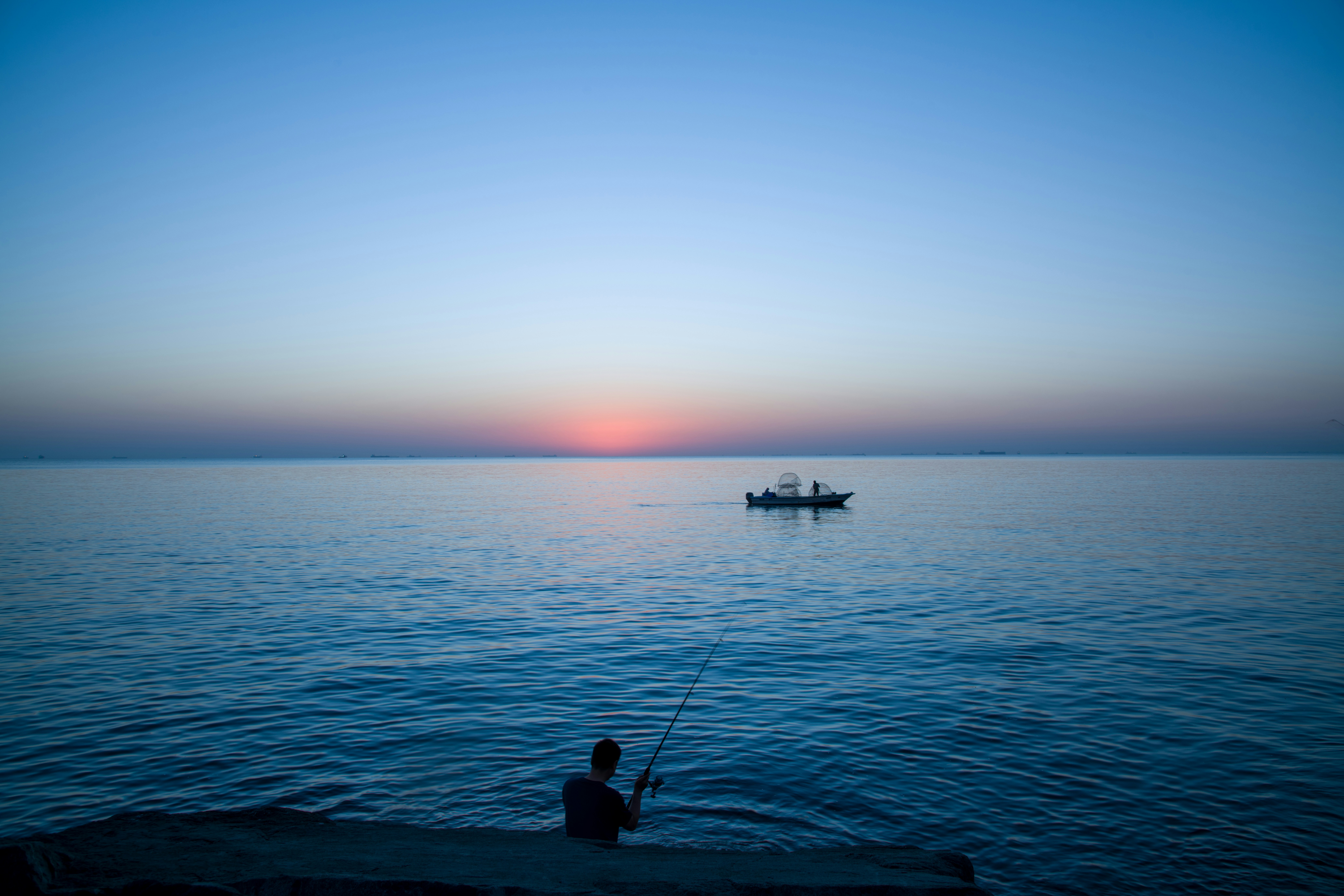 Evening Lure: A Fisherman's Quiet Cast Toward the Distant Boat