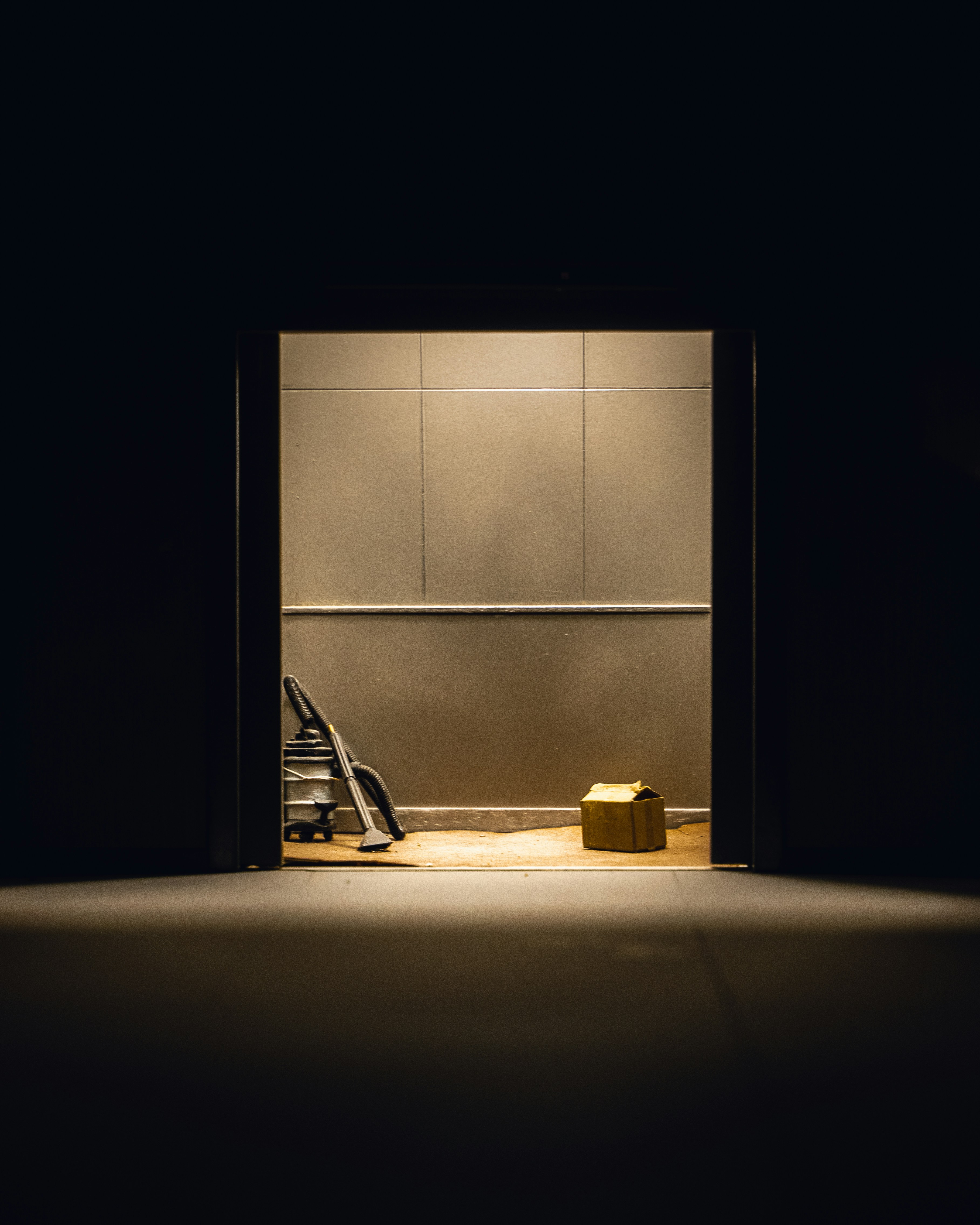 Dimly lit elevator shaft revealing a stack of chairs and a yellow box, evoking a sense of mystery and anticipation.
