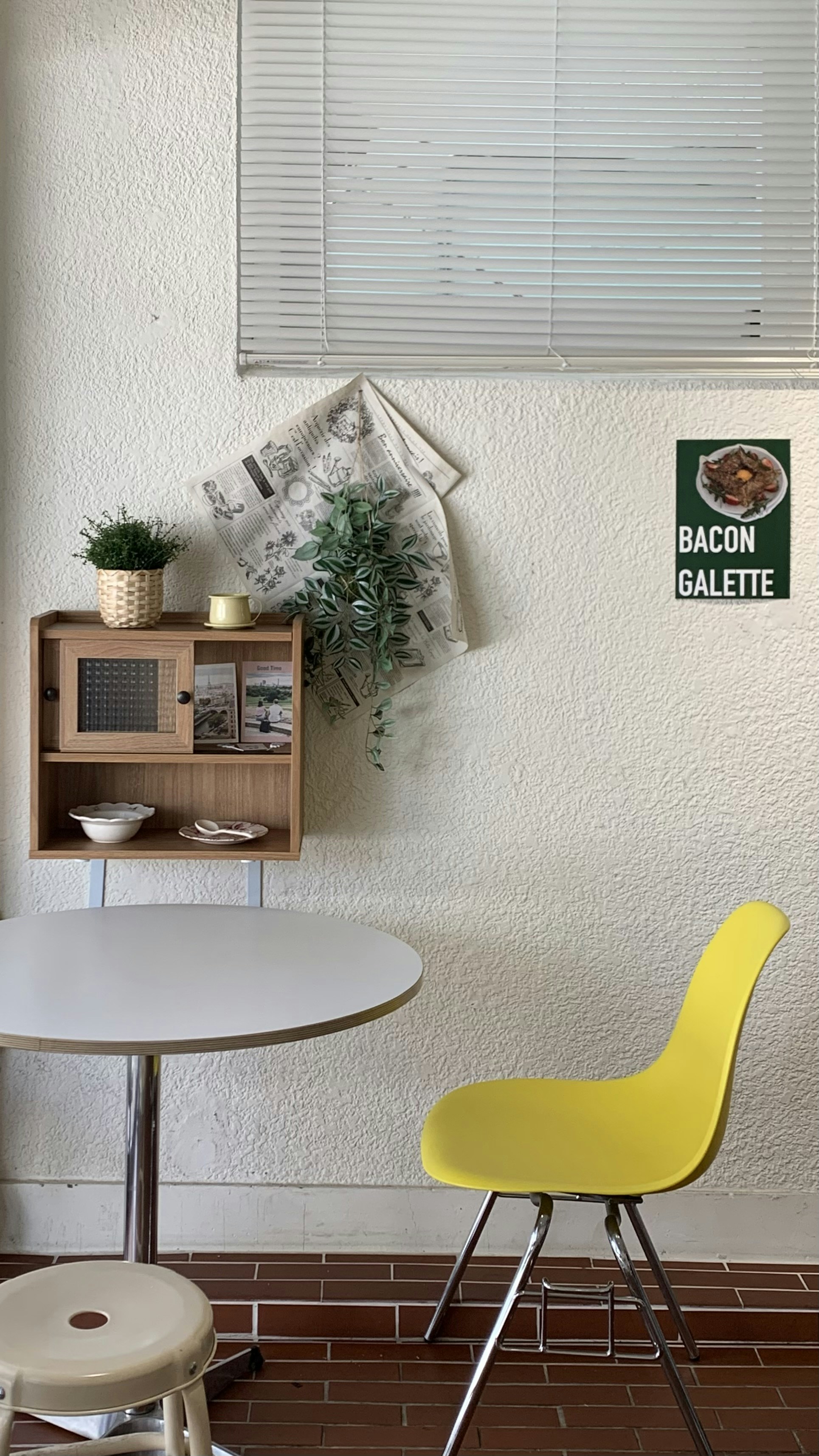 Cozy café corner featuring a round table, a vibrant yellow chair, and a wall adorned with decorative plants and a menu sign. The arrangement invites a sense of warmth and tranquility.