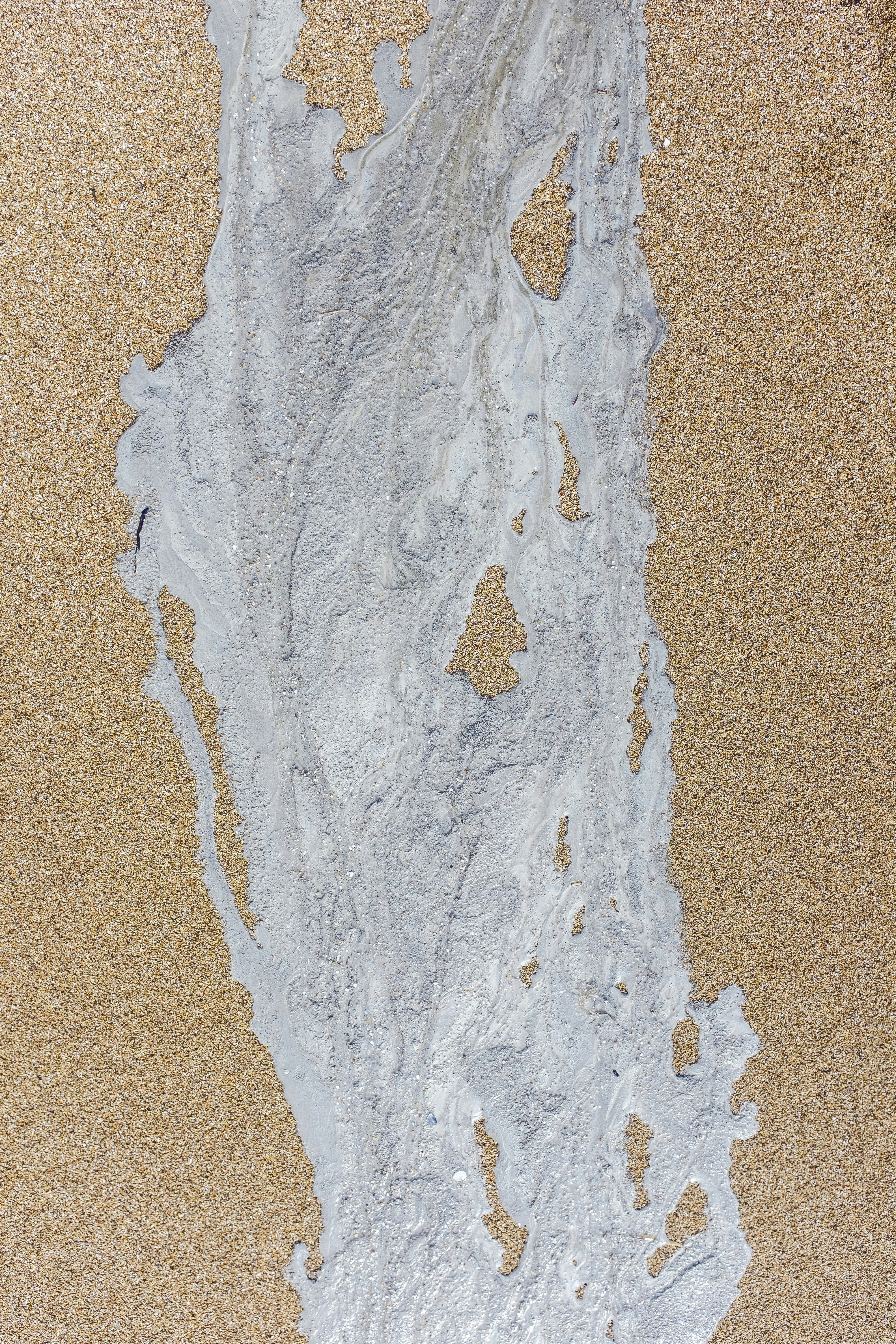 Foamy water trails cascading over fine golden sand, capturing the ebb and flow of the tide. The texture contrasts create a serene coastal scene.