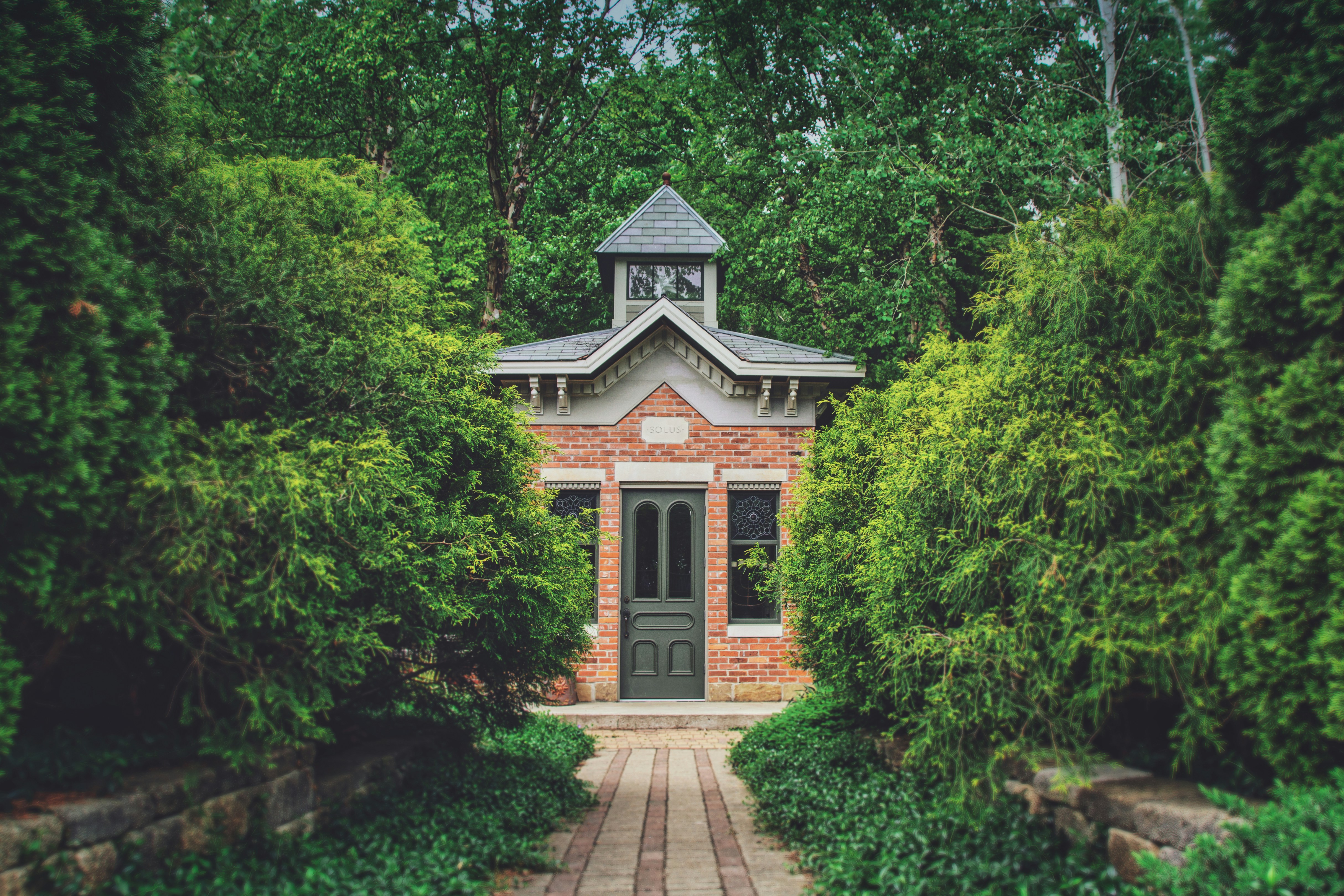 Charming brick building framed by lush greenery and a stone pathway leading to its door.
