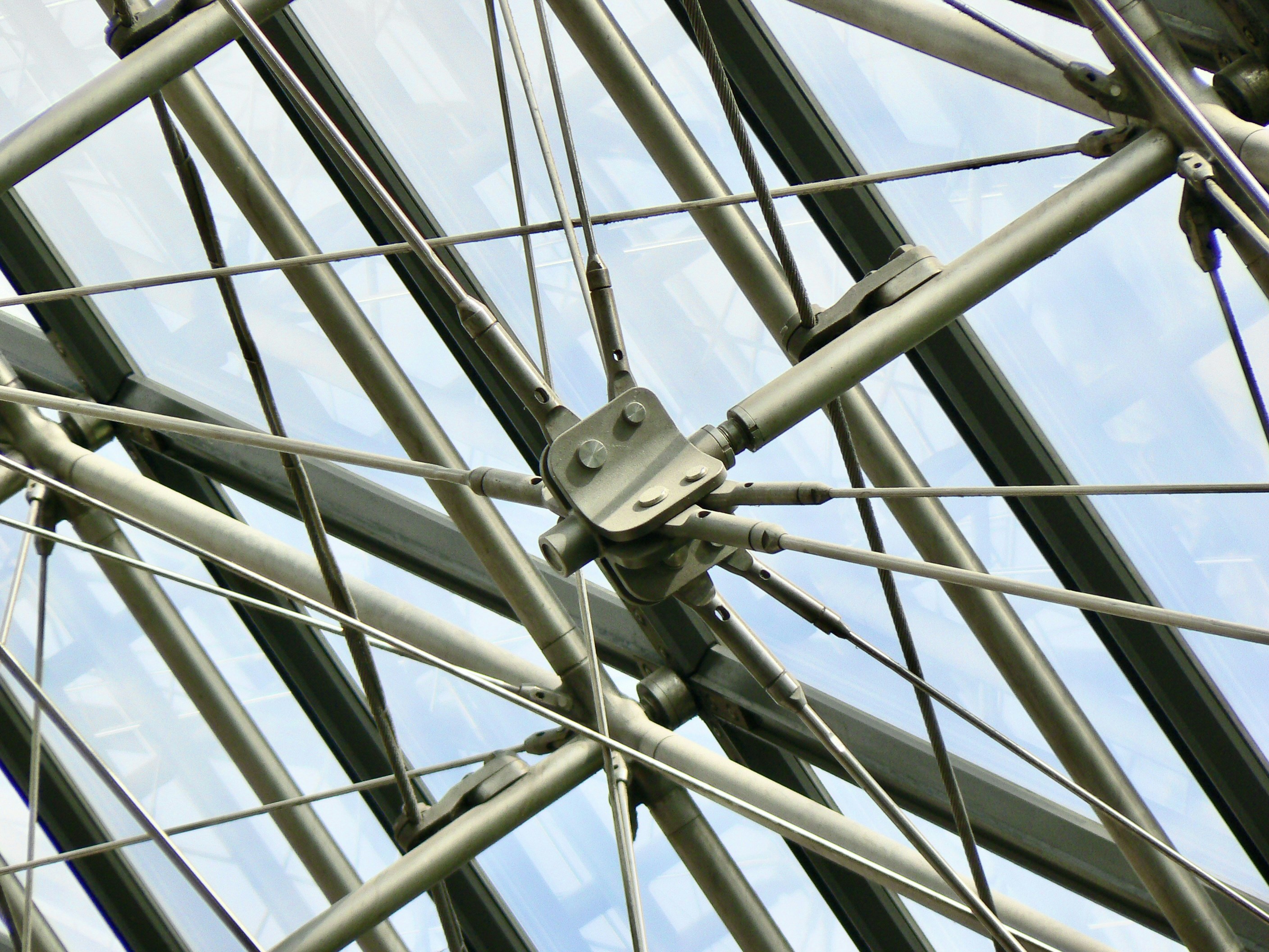 Close-up of metallic support structures intersecting beneath a glass canopy, showcasing engineering precision and design.