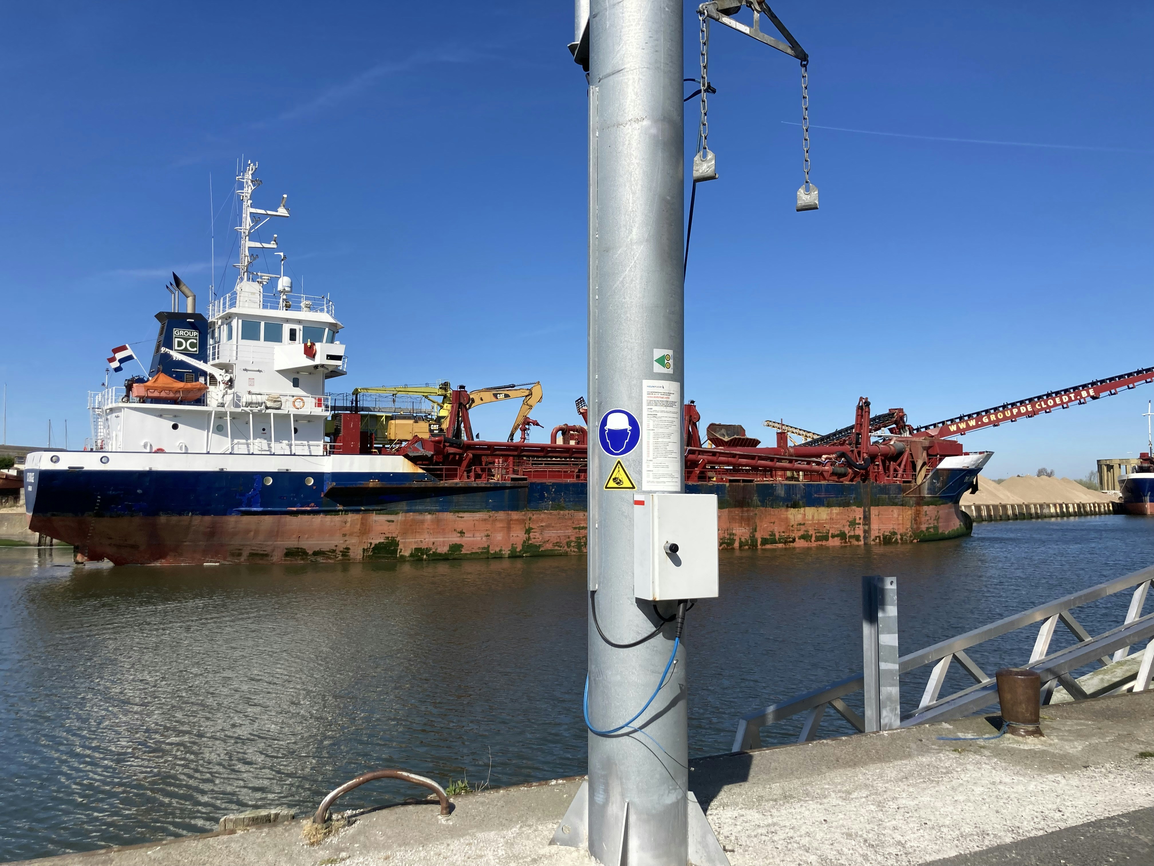 Harbor Sentinel: A Red-Hulled Cargo Vessel Framed by a Foreground Pier Column