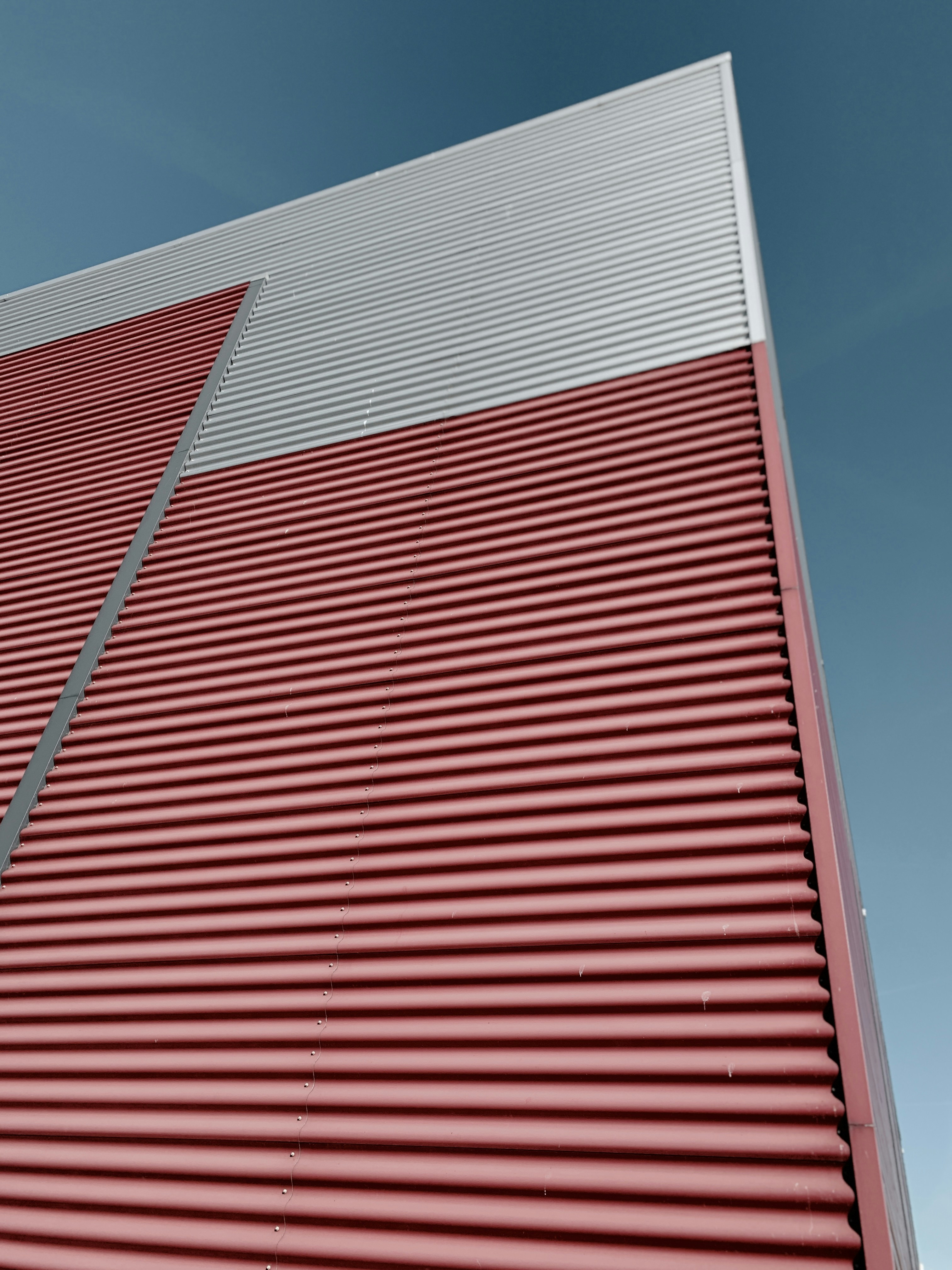 Abstract architectural detail showcasing contrasting red and silver corrugated panels against a clear sky.