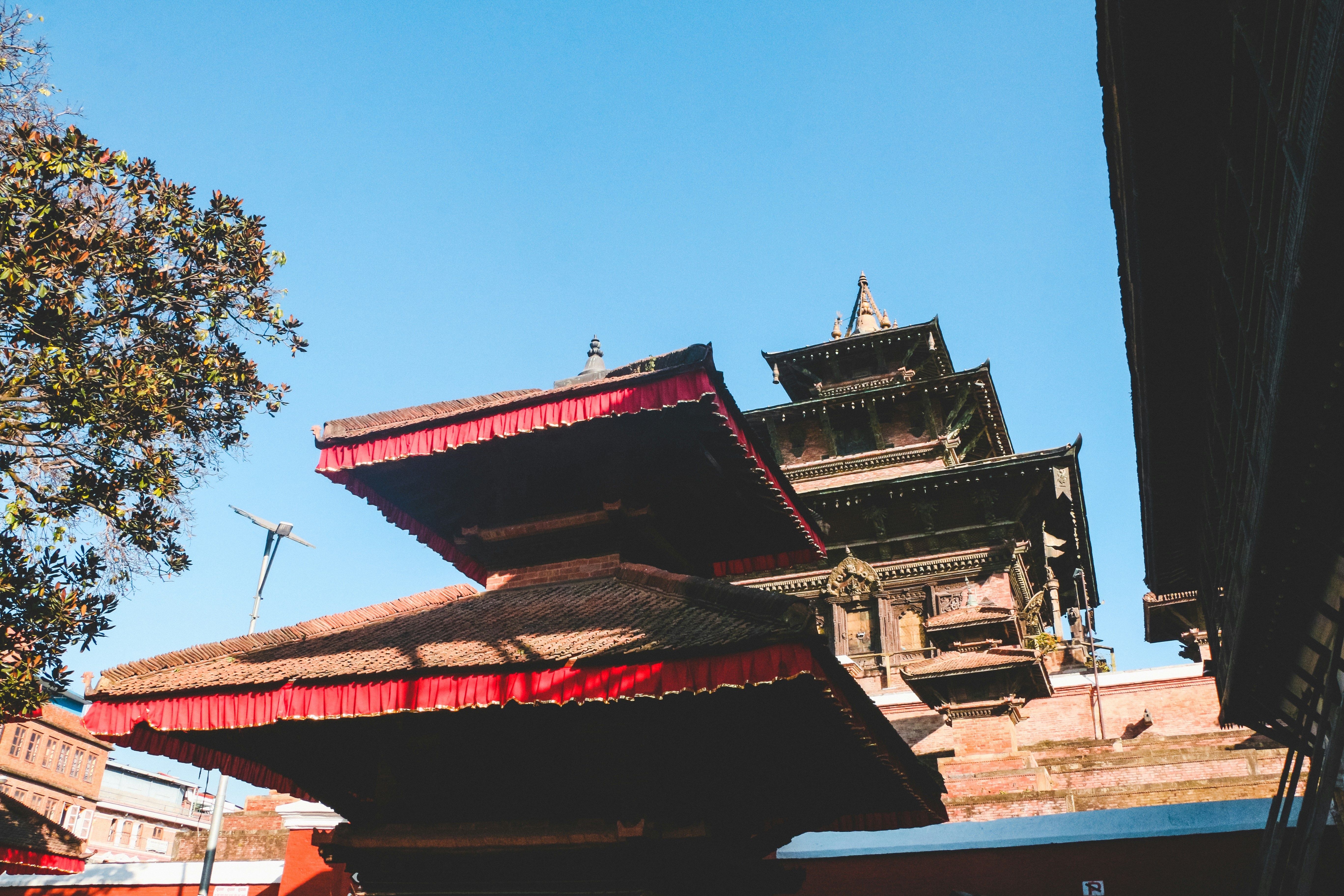 Intricate Nepali temple structure framed by vibrant red canopies under a clear blue sky.