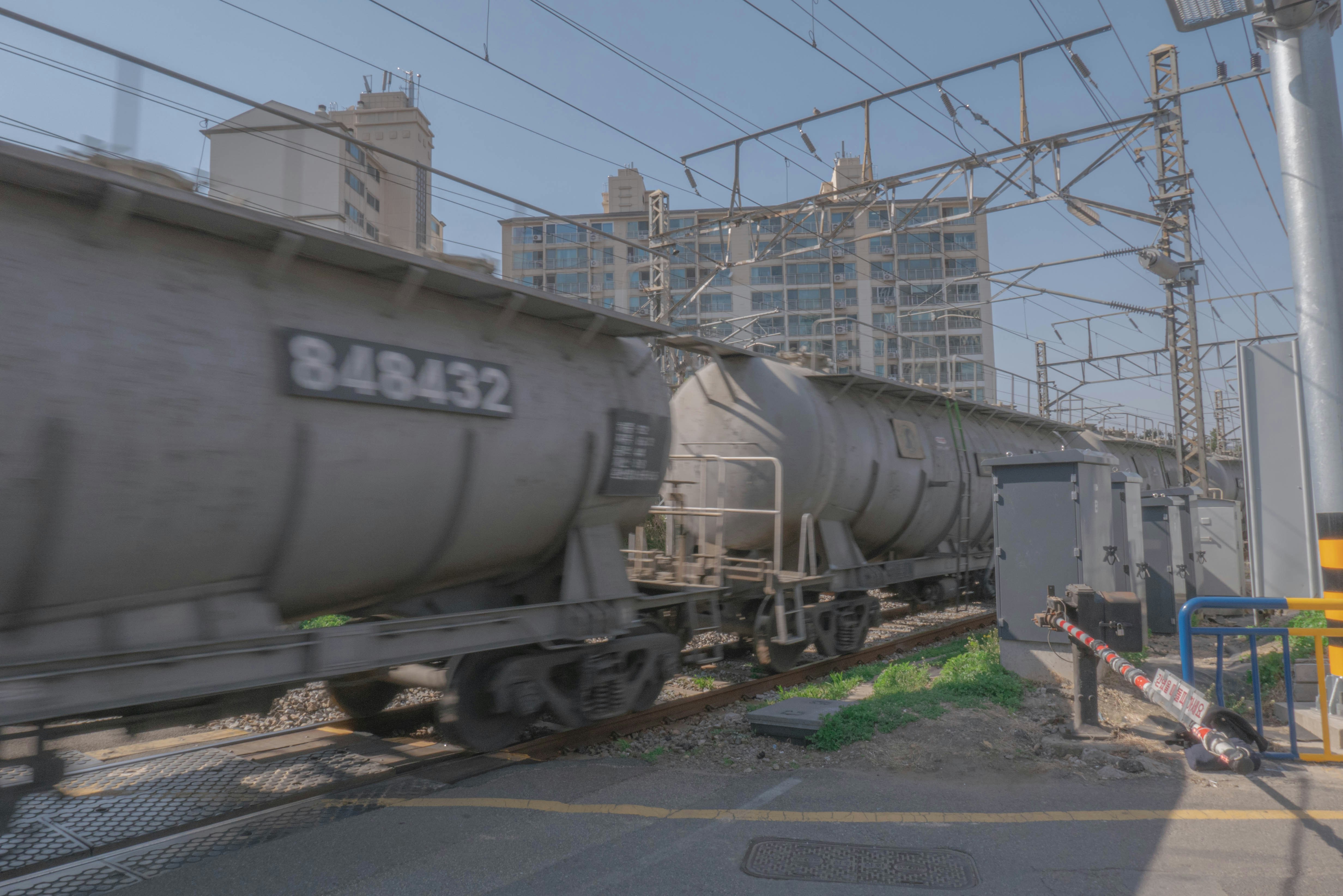 Freight train passing through an urban area, with modern buildings in the background and railway infrastructure visible.
