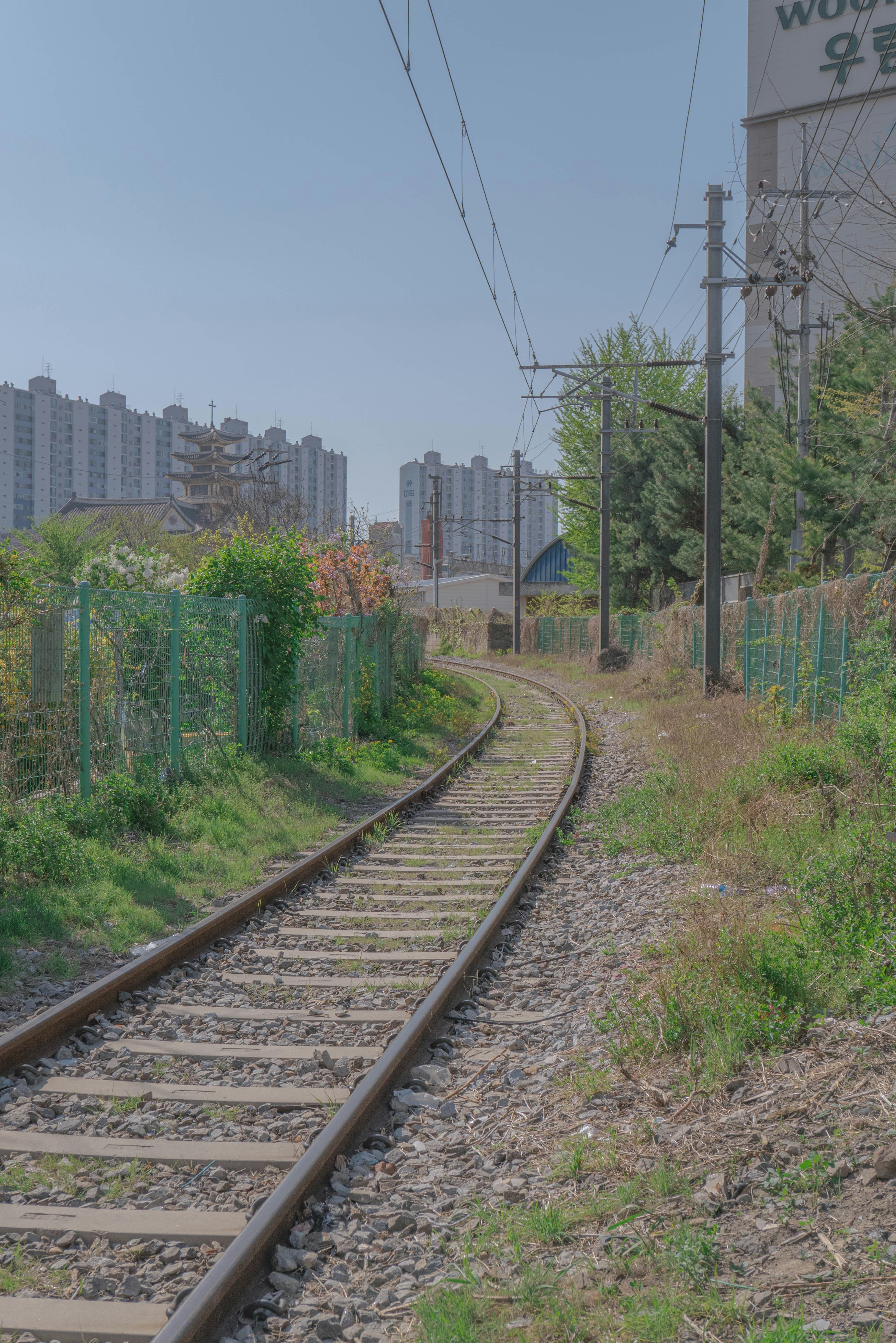 Winding railway tracks bordered by greenery and urban structures under a clear sky.