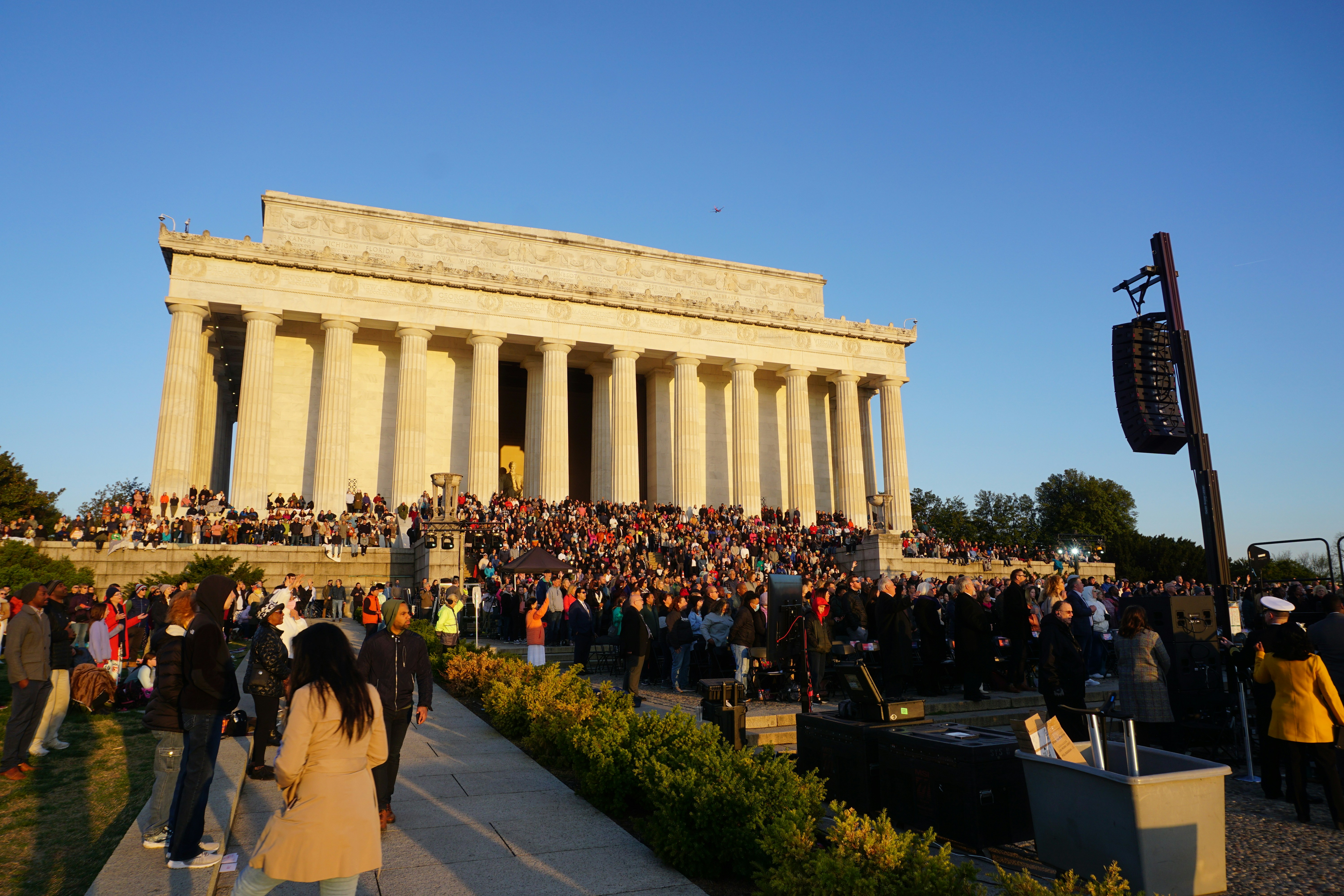 Crowd gathered at the Lincoln Memorial during an evening event, with the iconic structure illuminated by the setting sun.