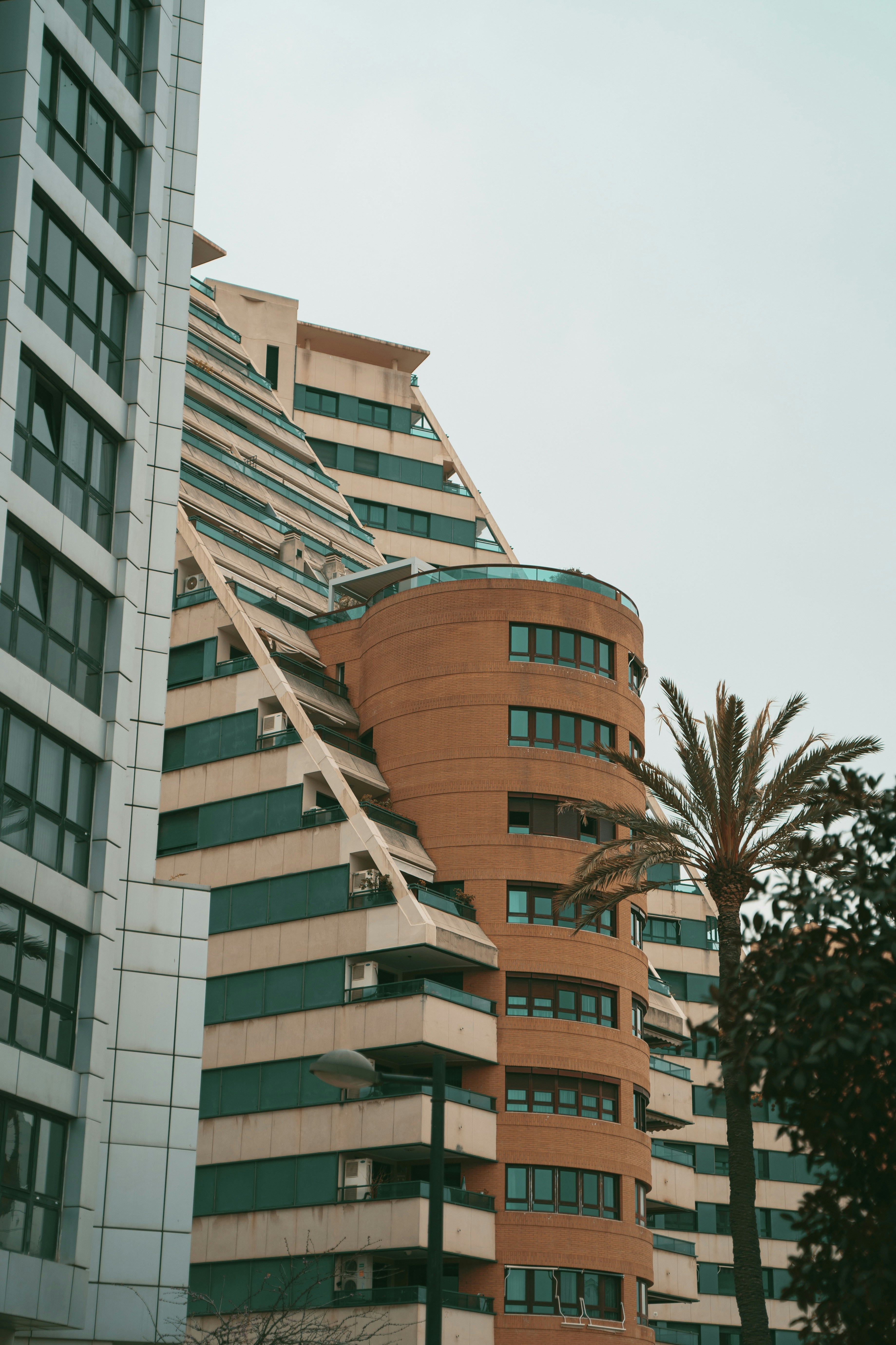 Modern buildings showcasing unique geometric shapes and contrasting materials, framed by palm trees.