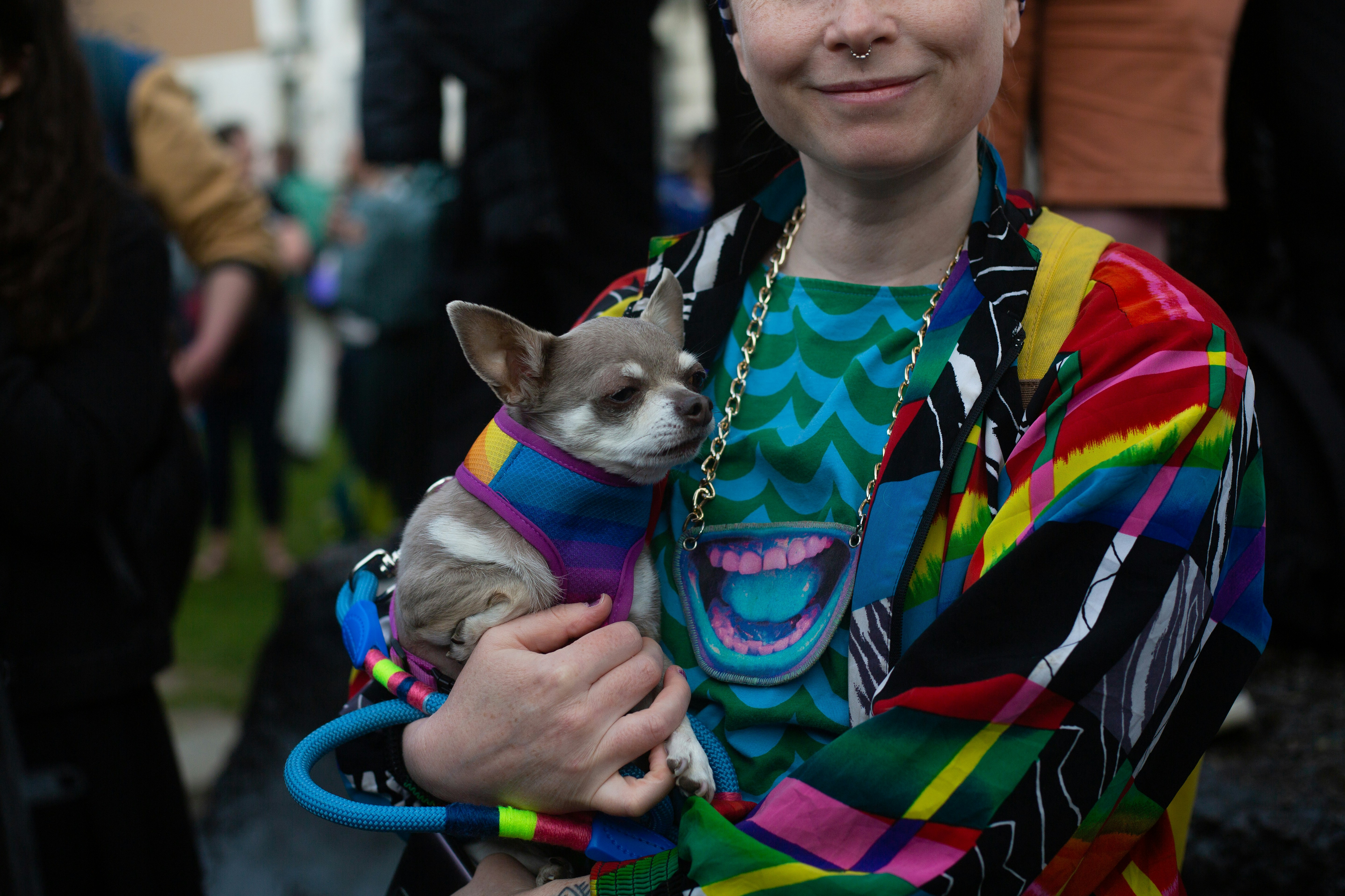 Woman in colorful attire holding a small dog wrapped in a matching rainbow sweater.