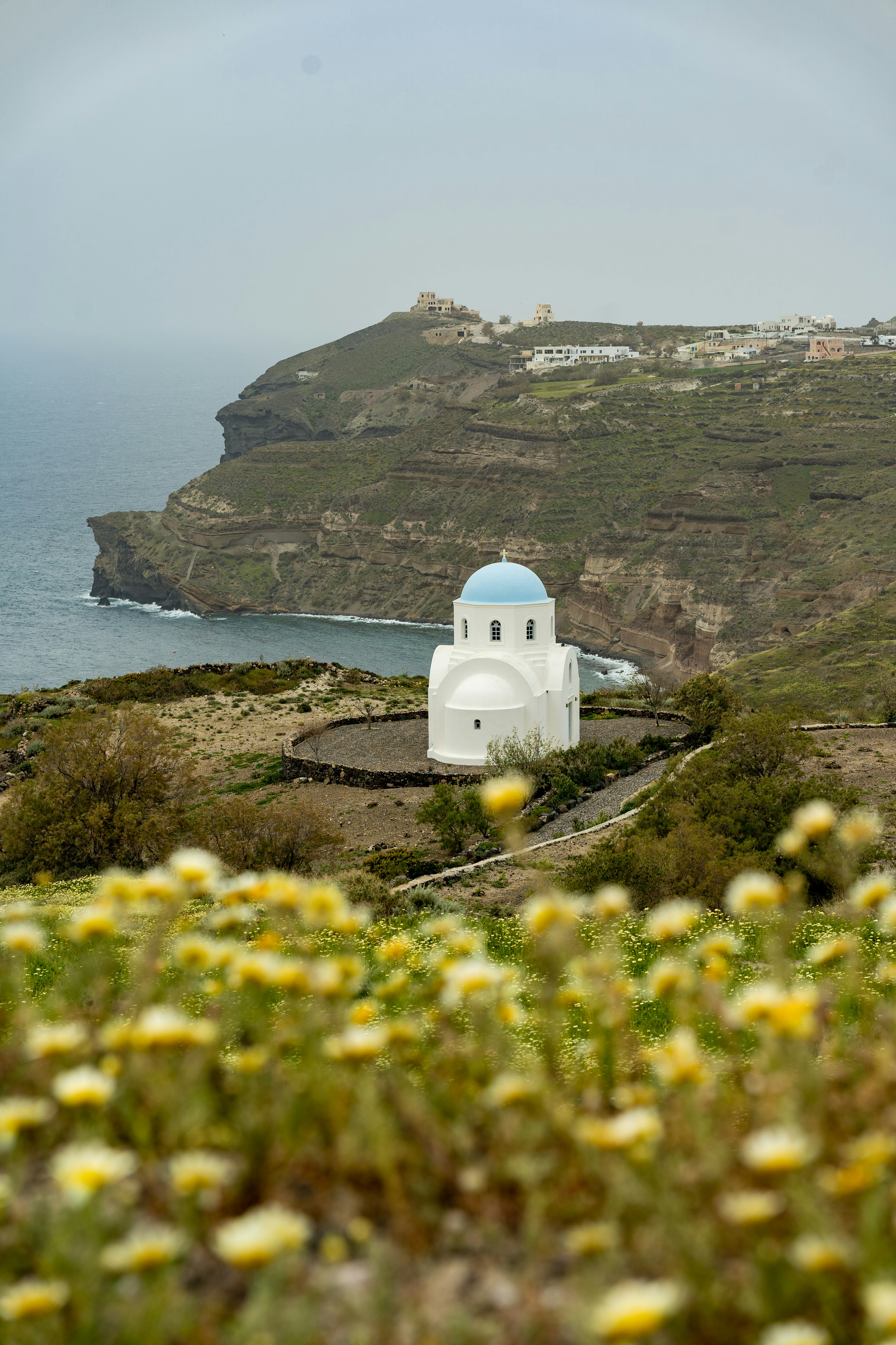 Blue-Domed Chapel on a Cliffside: Aegean Vista Framed by Spring Blooms