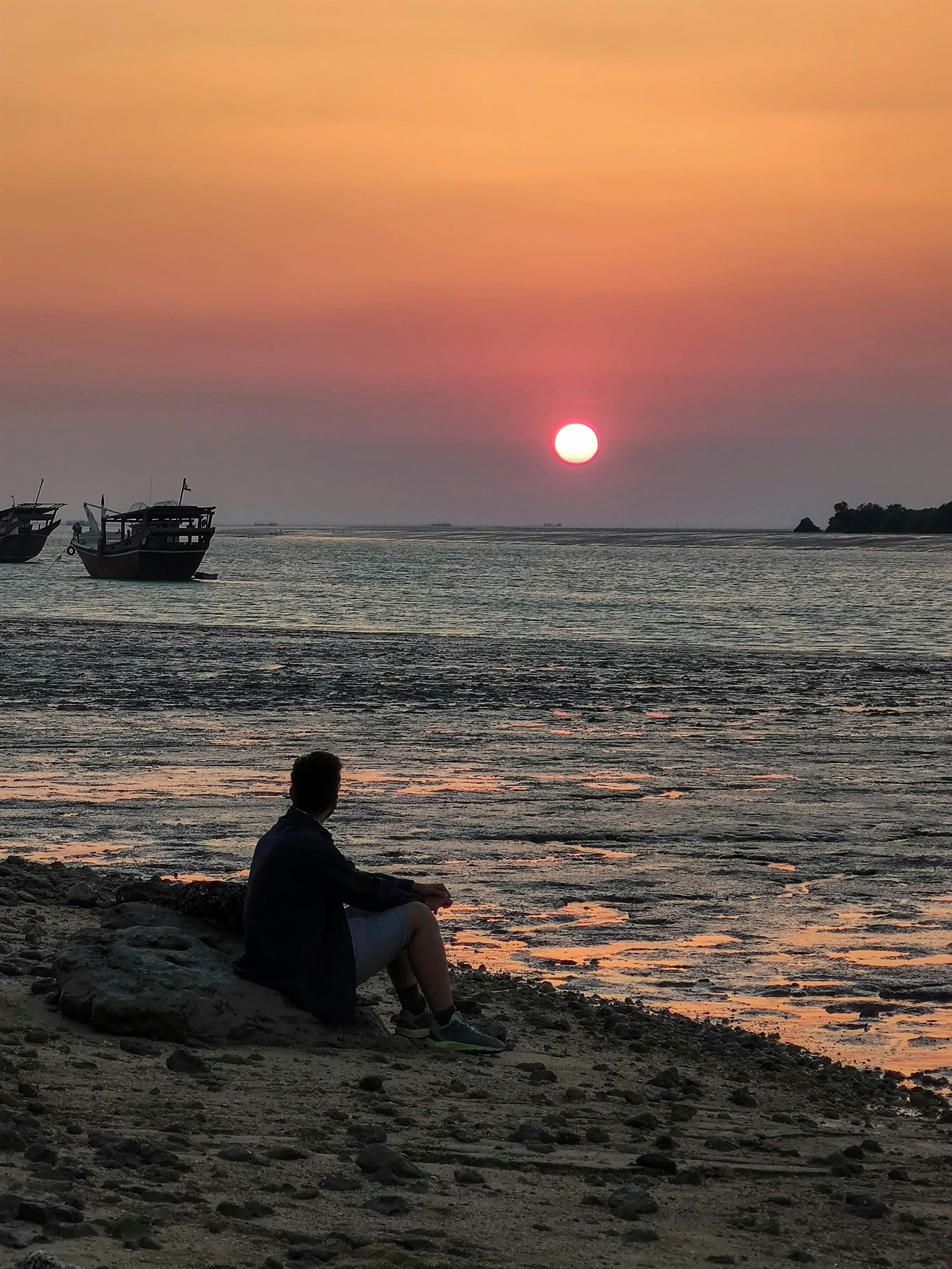 A man sitting on the beach watching the sunset photo – Free Nature ...