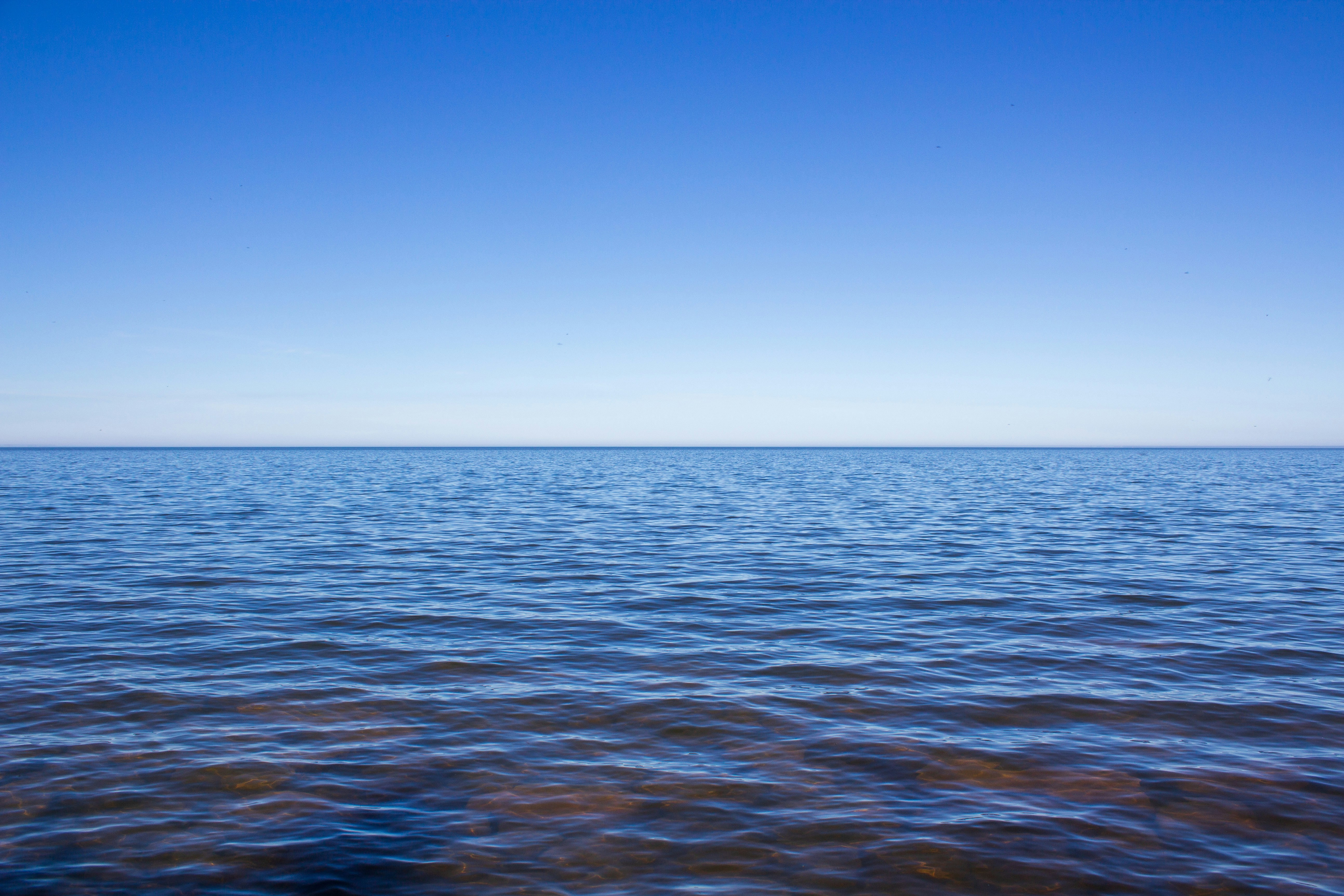 A body of water with a blue sky in the background photo – Free Blue ...