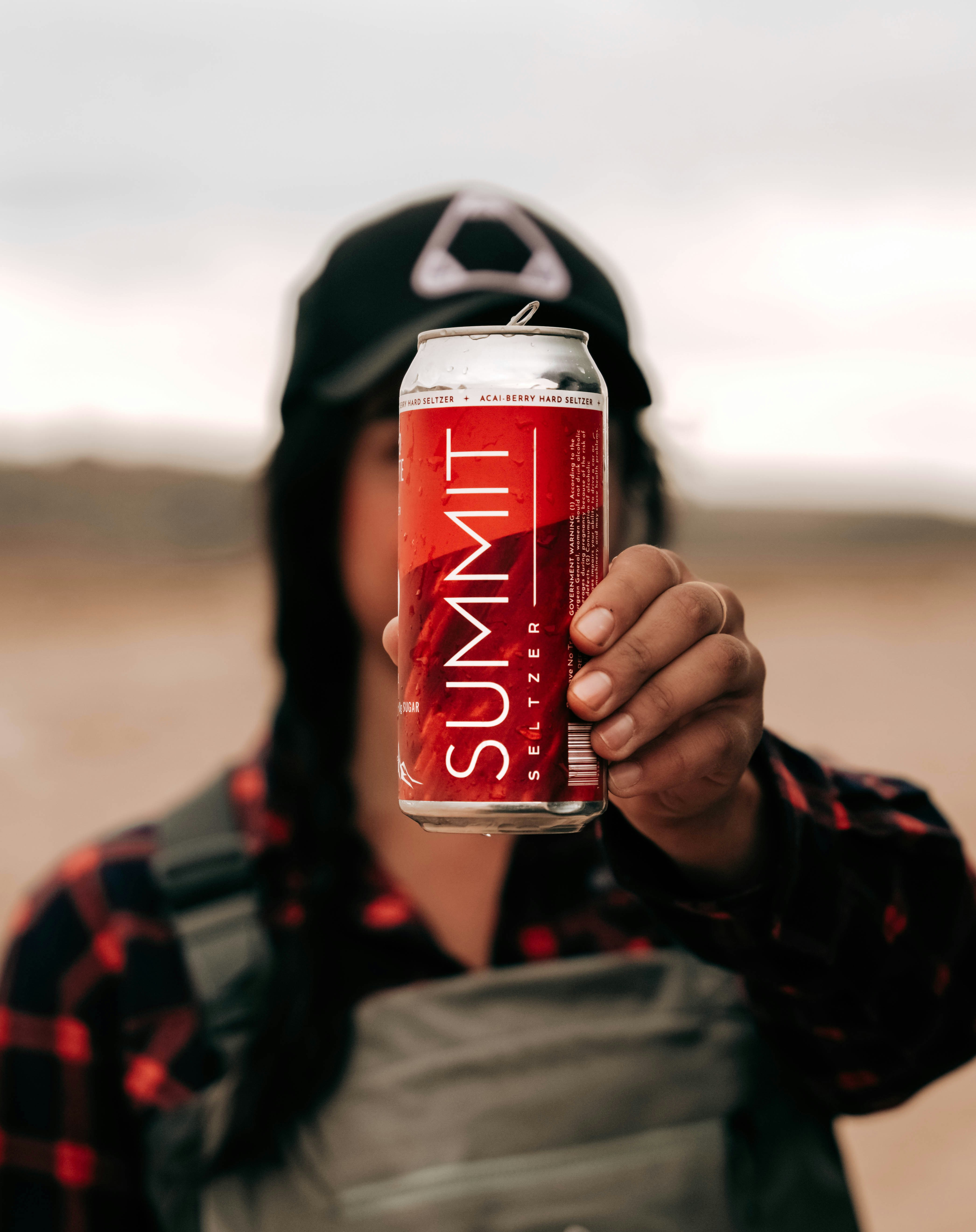 A person holds a can of Summit Seltzer in a casual outdoor setting, showcasing the vibrant packaging against a blurred background. 