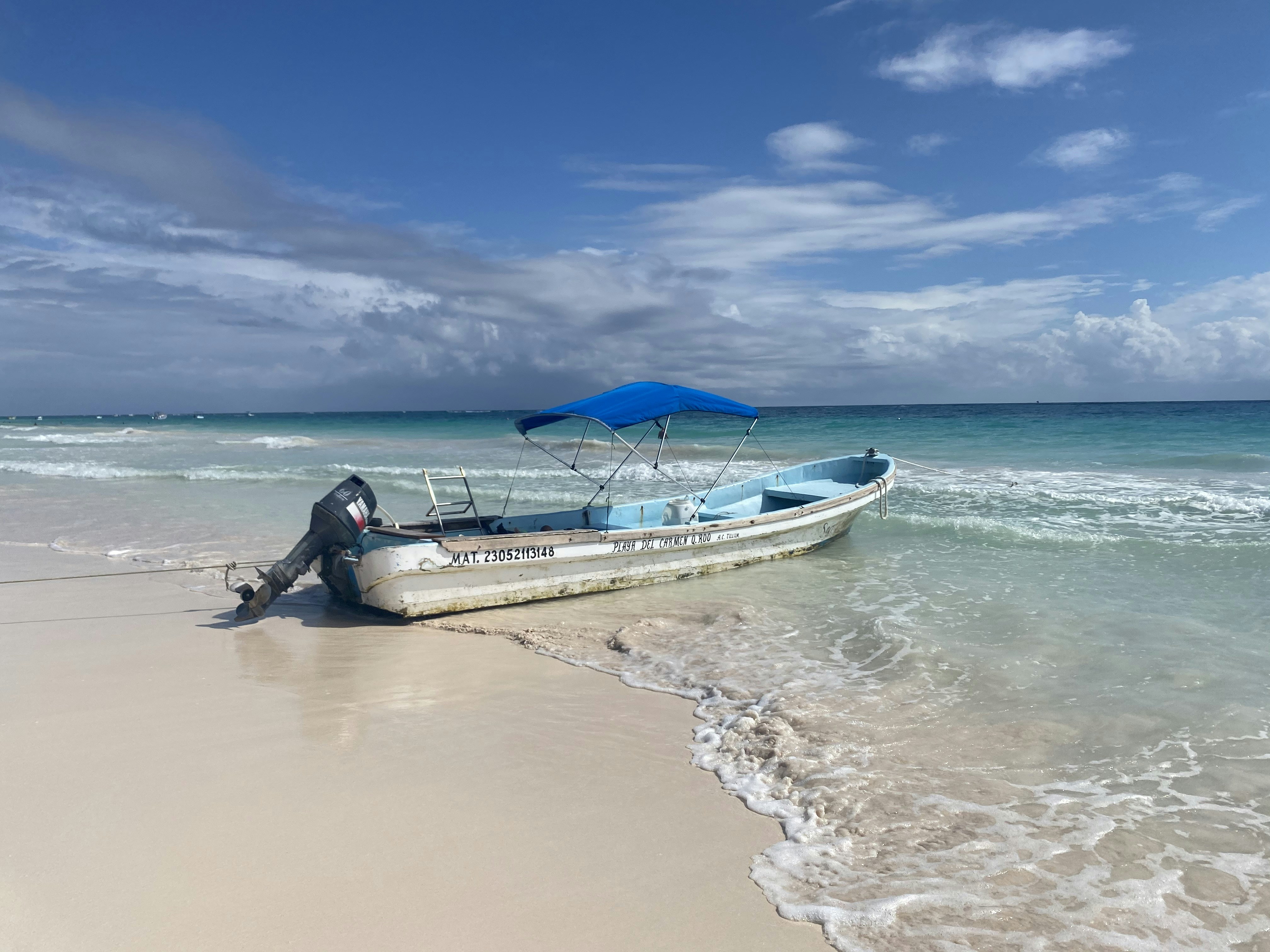 A fishing boat anchored on a tranquil beach, with gentle waves lapping against the shore under a bright blue sky.
