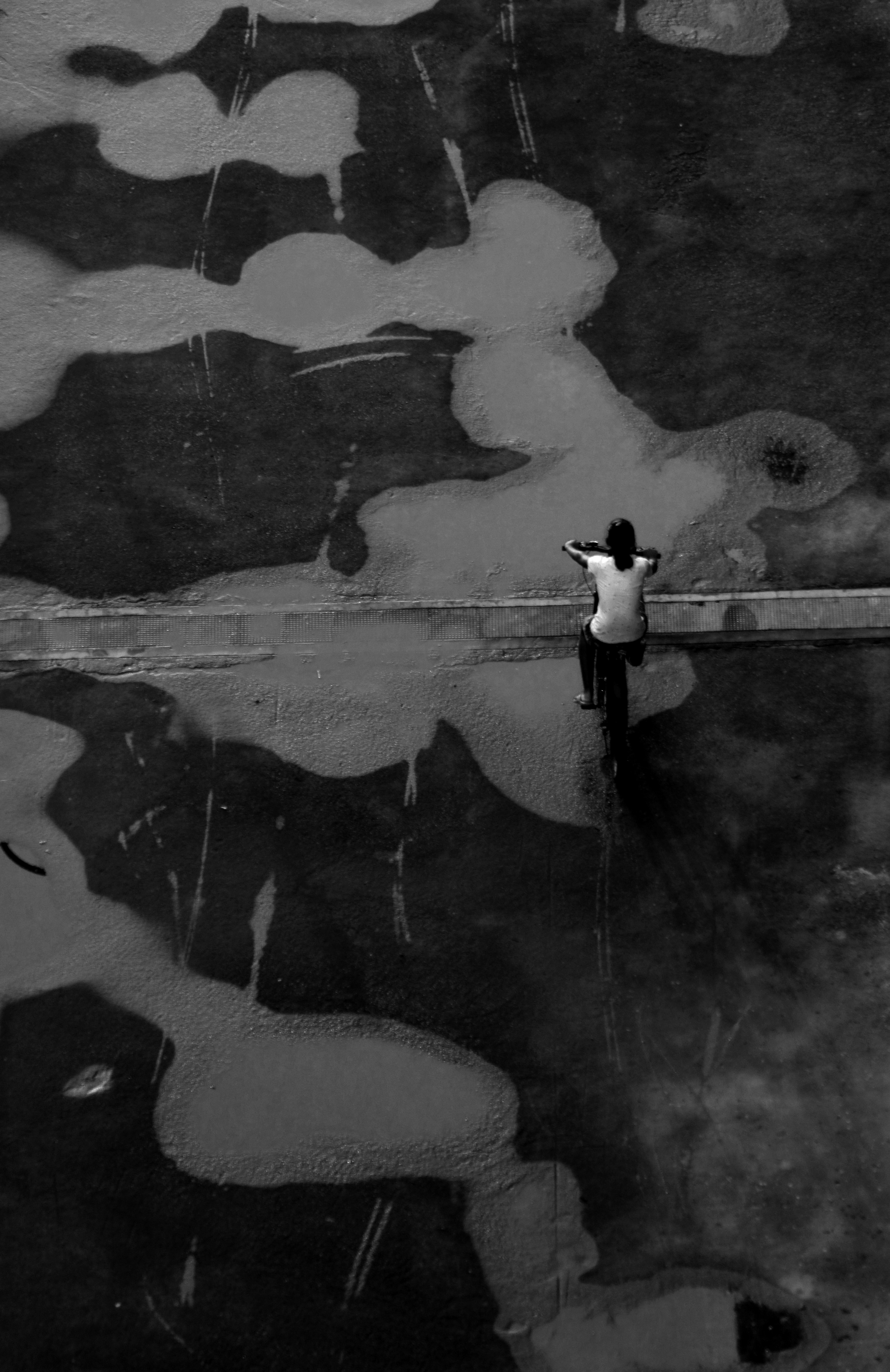A cyclist traverses a wet surface, creating a striking contrast with abstract patterns formed by water. The monochrome palette enhances the visual narrative.