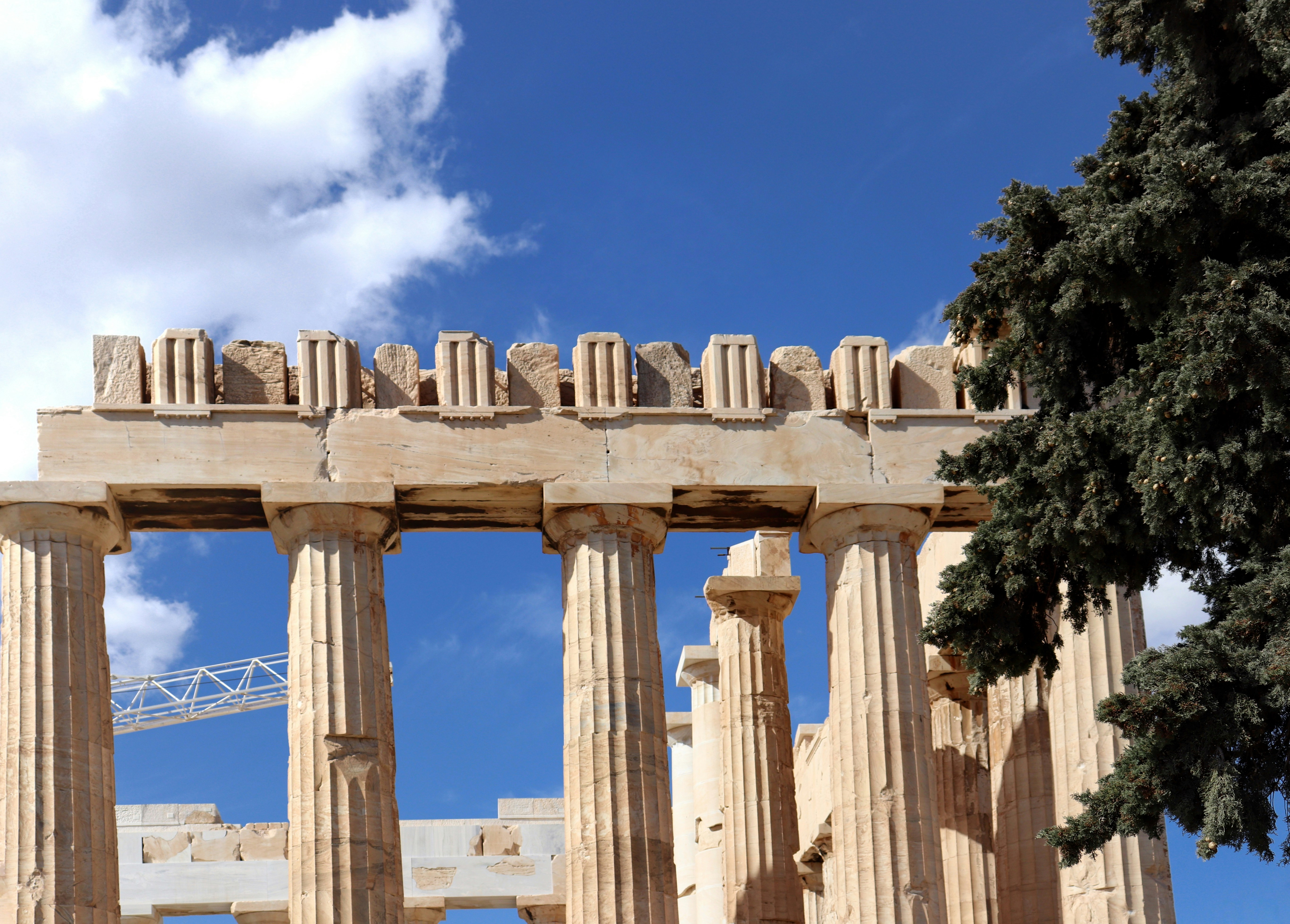 Ancient stone columns of a historic structure beneath a bright blue sky with scattered clouds.