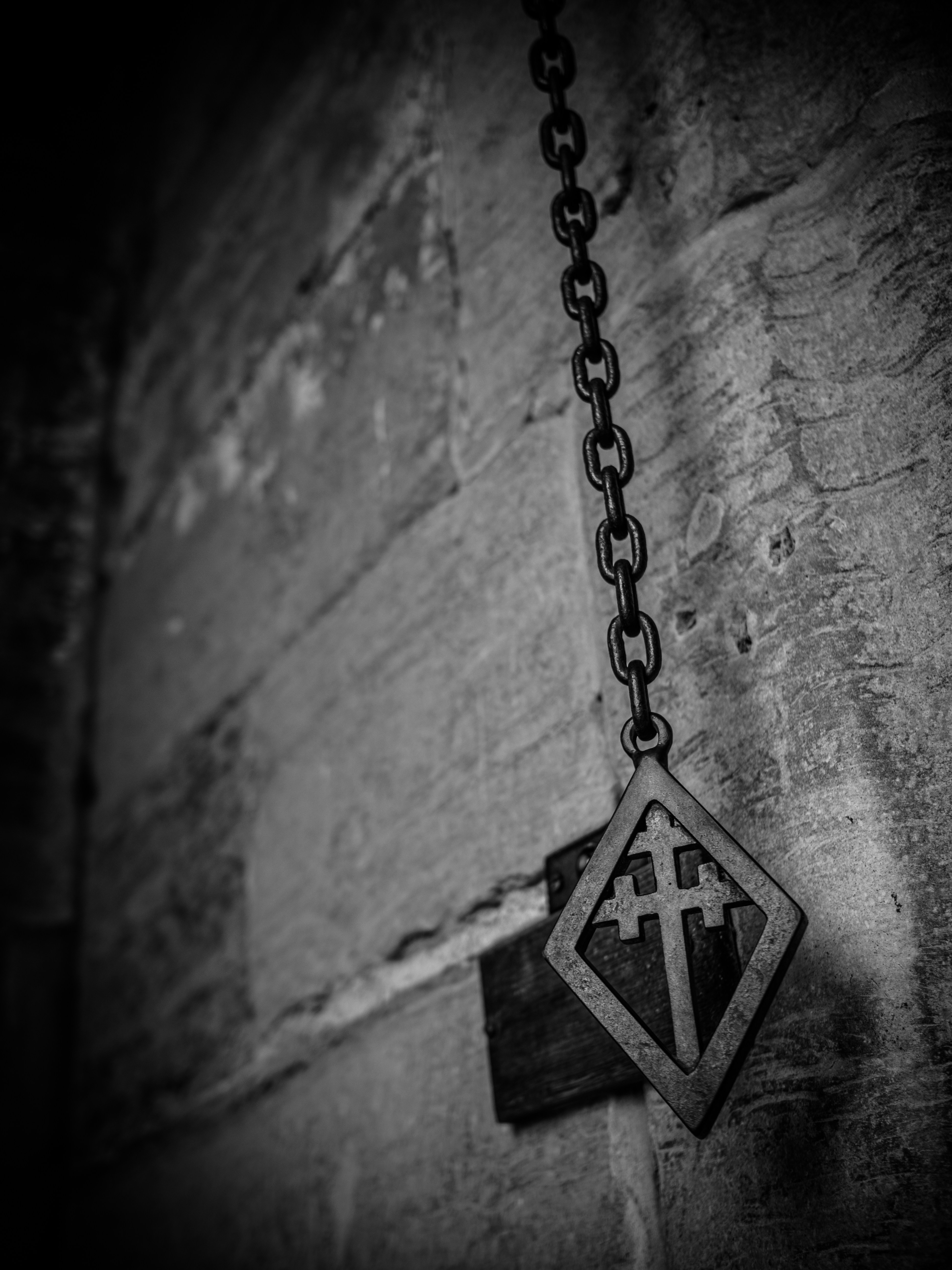 Monochrome cross pendant hanging from a chain against a textured wooden background.