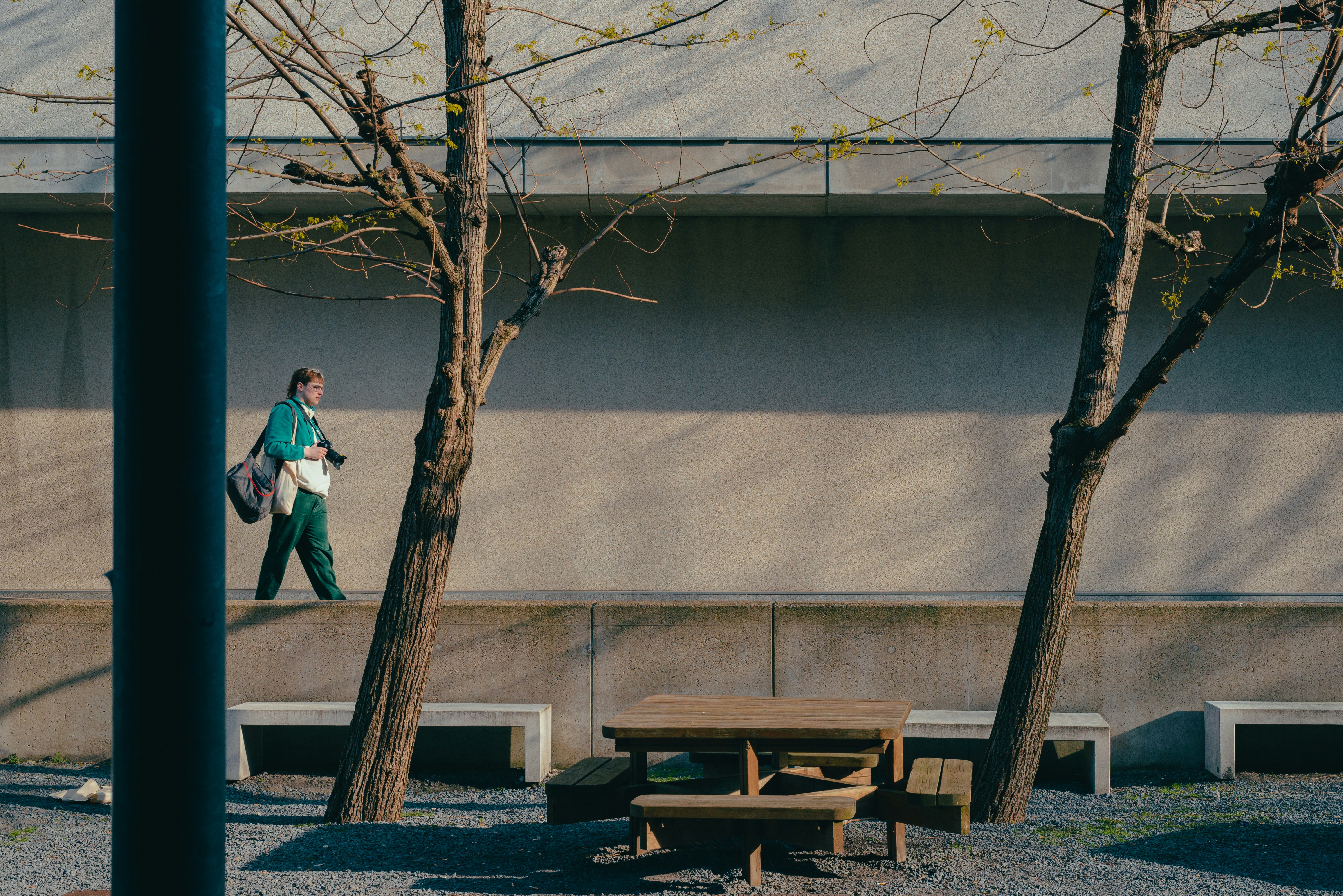 Teal-clad commuter strides along a sunlit urban wall