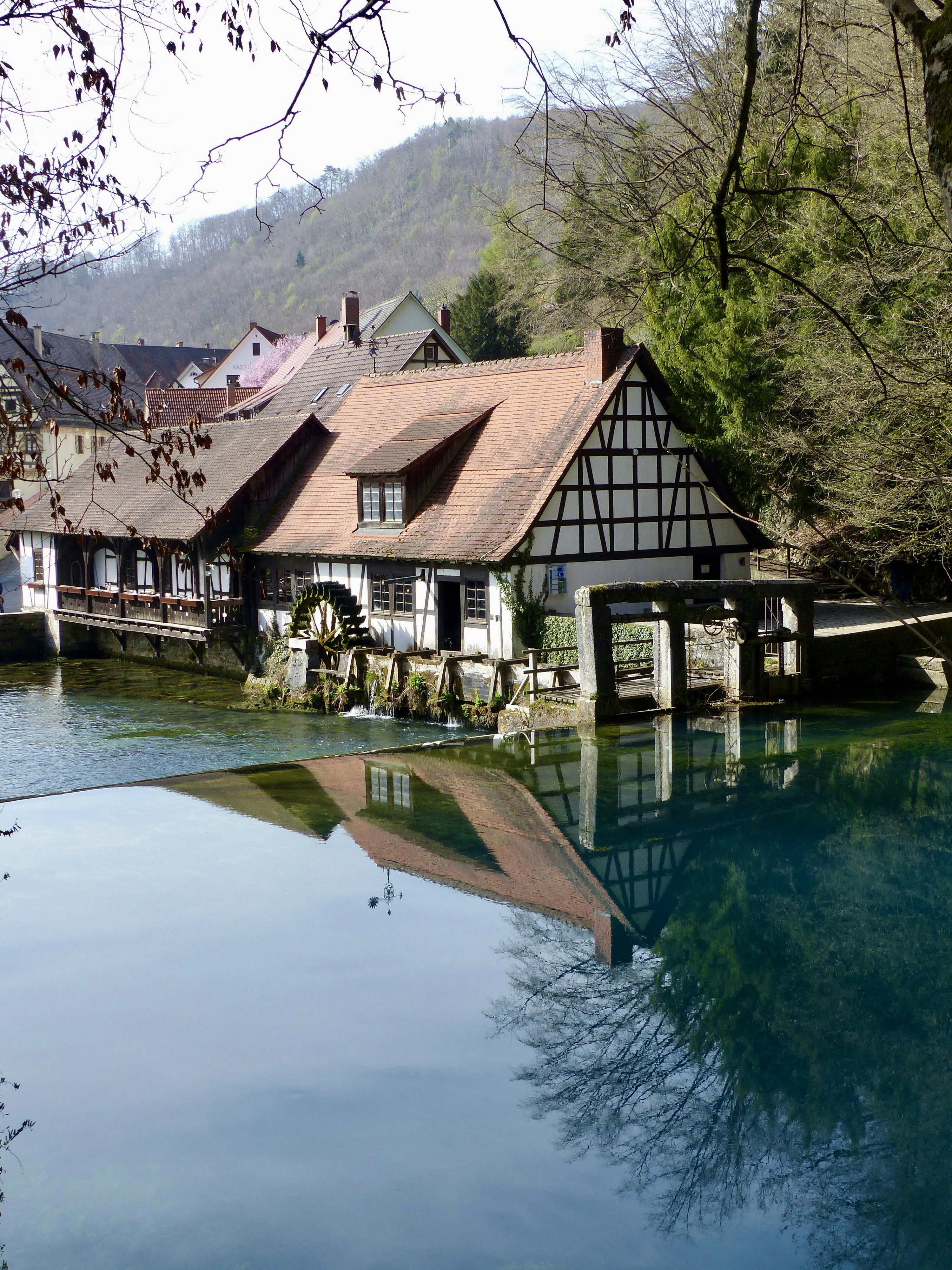 Charming historical building by a serene river, reflecting on the water's surface under a clear sky.
