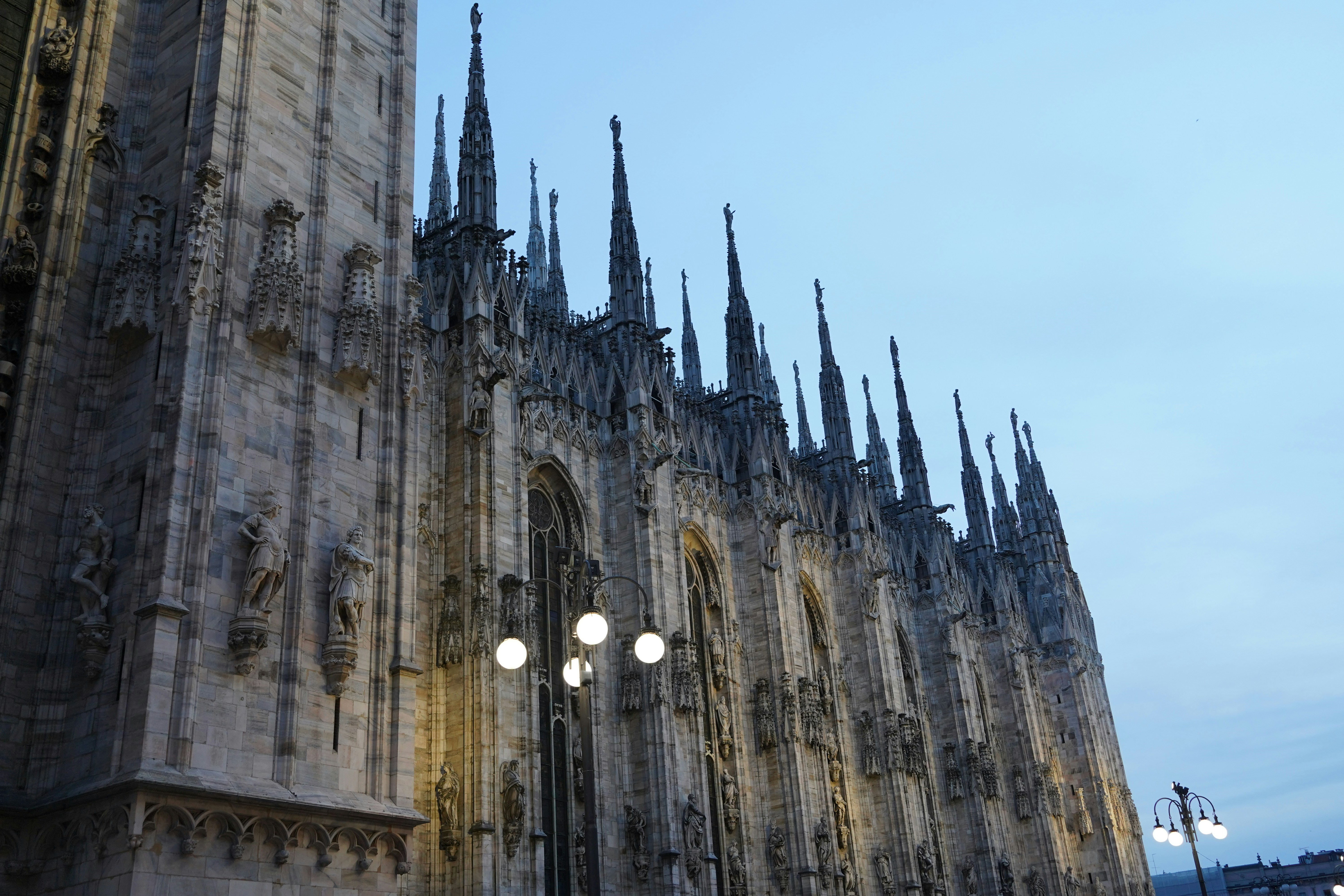 Intricate Gothic architecture of a cathedral's facade illuminated by soft evening light, showcasing detailed sculptures and towering spires.