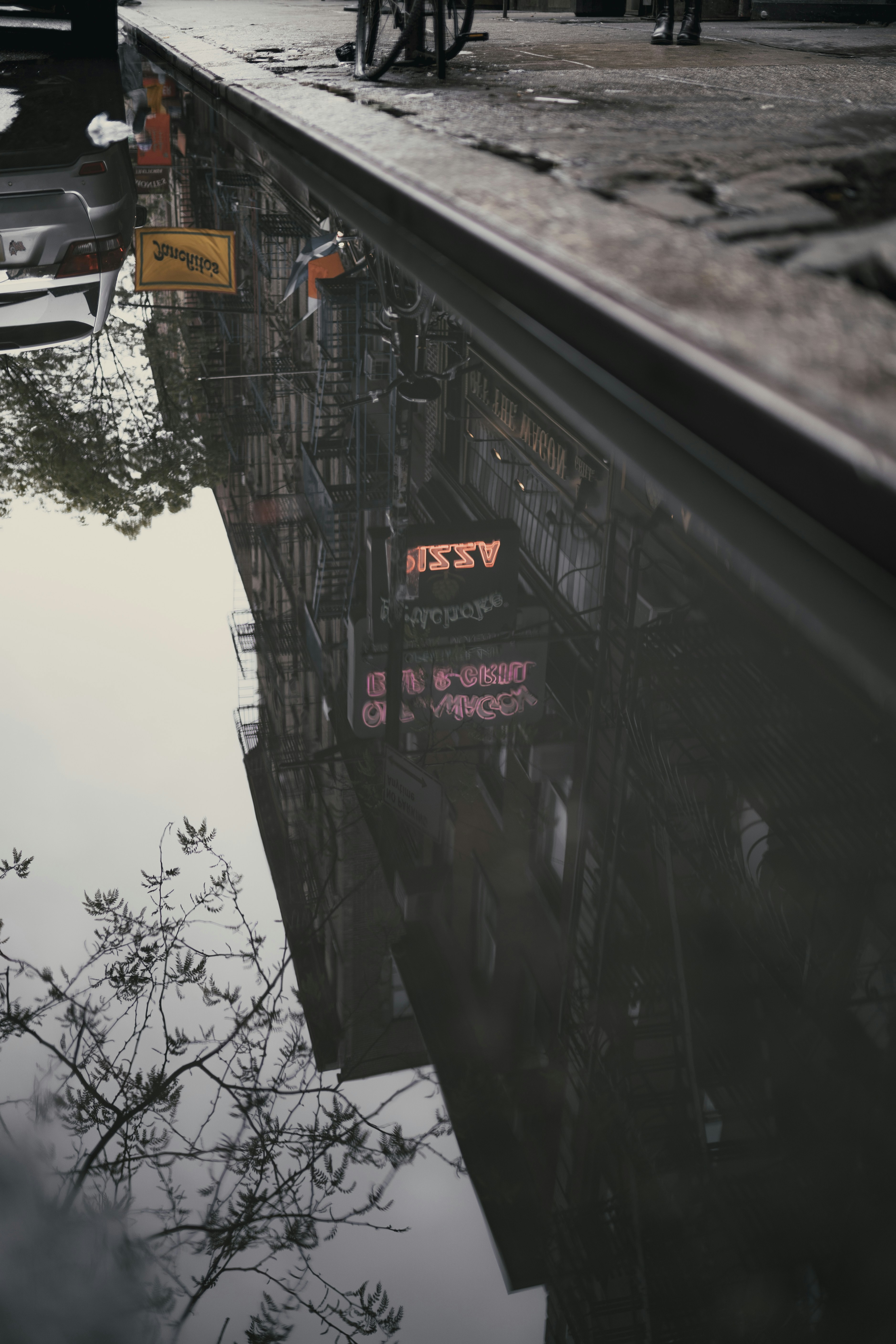 Cityscape reflected in a puddle, showcasing vibrant neon signs and urban details. The scene captures the essence of a rainy day in a bustling neighborhood.