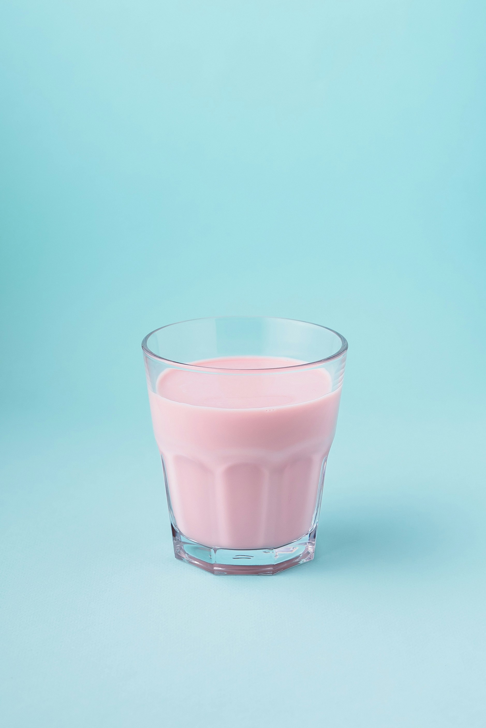 Glass filled with creamy pink beverage set against a soft blue background.