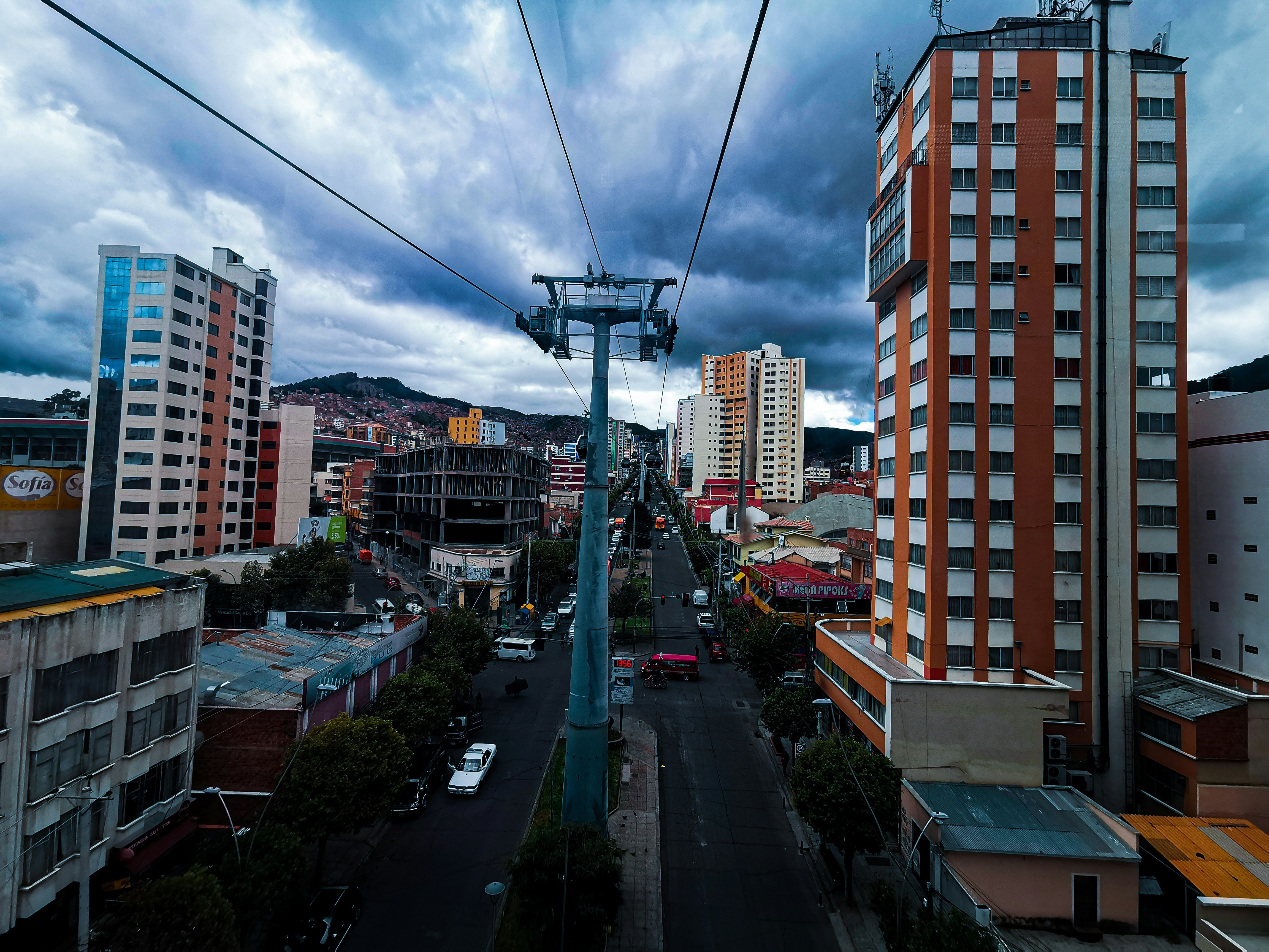 Aerial view of a bustling urban street lined with buildings and vehicles, framed by a dramatic sky filled with clouds.