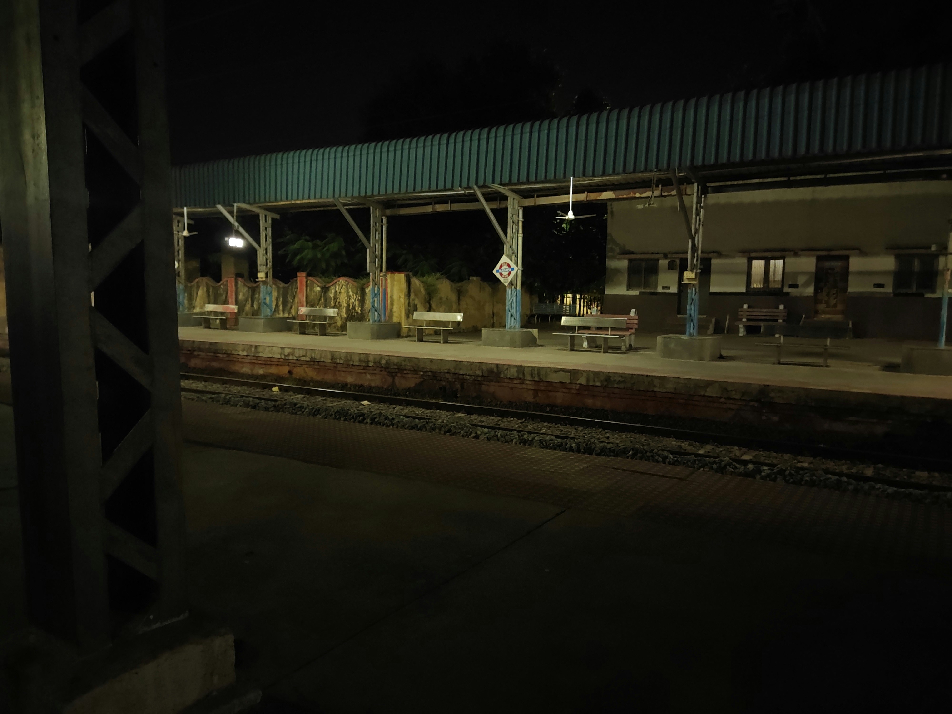 Dimly lit train station platform with empty benches and a hint of colorful murals in the background. The atmosphere conveys solitude and anticipation.
