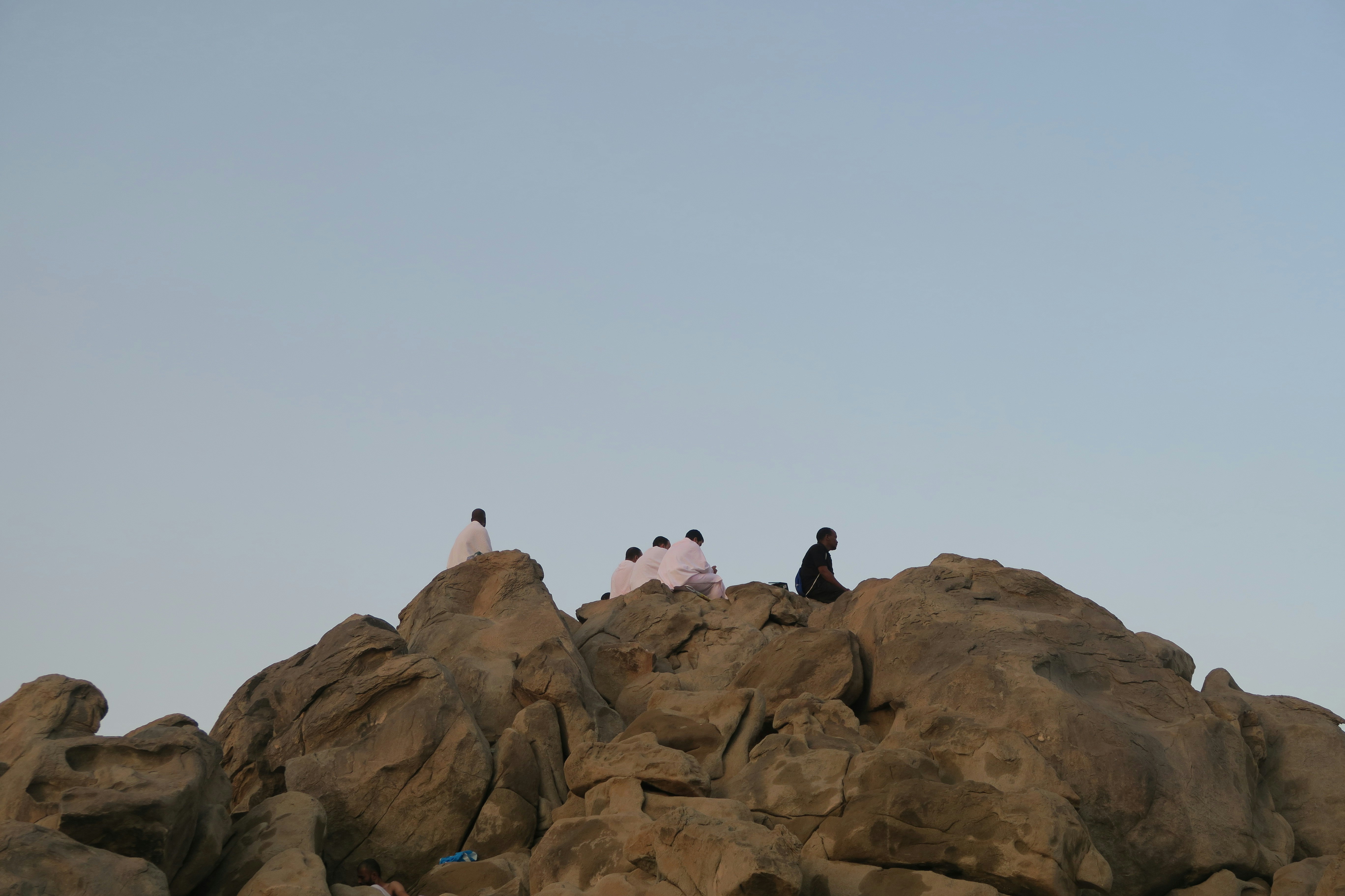 People sitting atop a large rock under a clear sky.