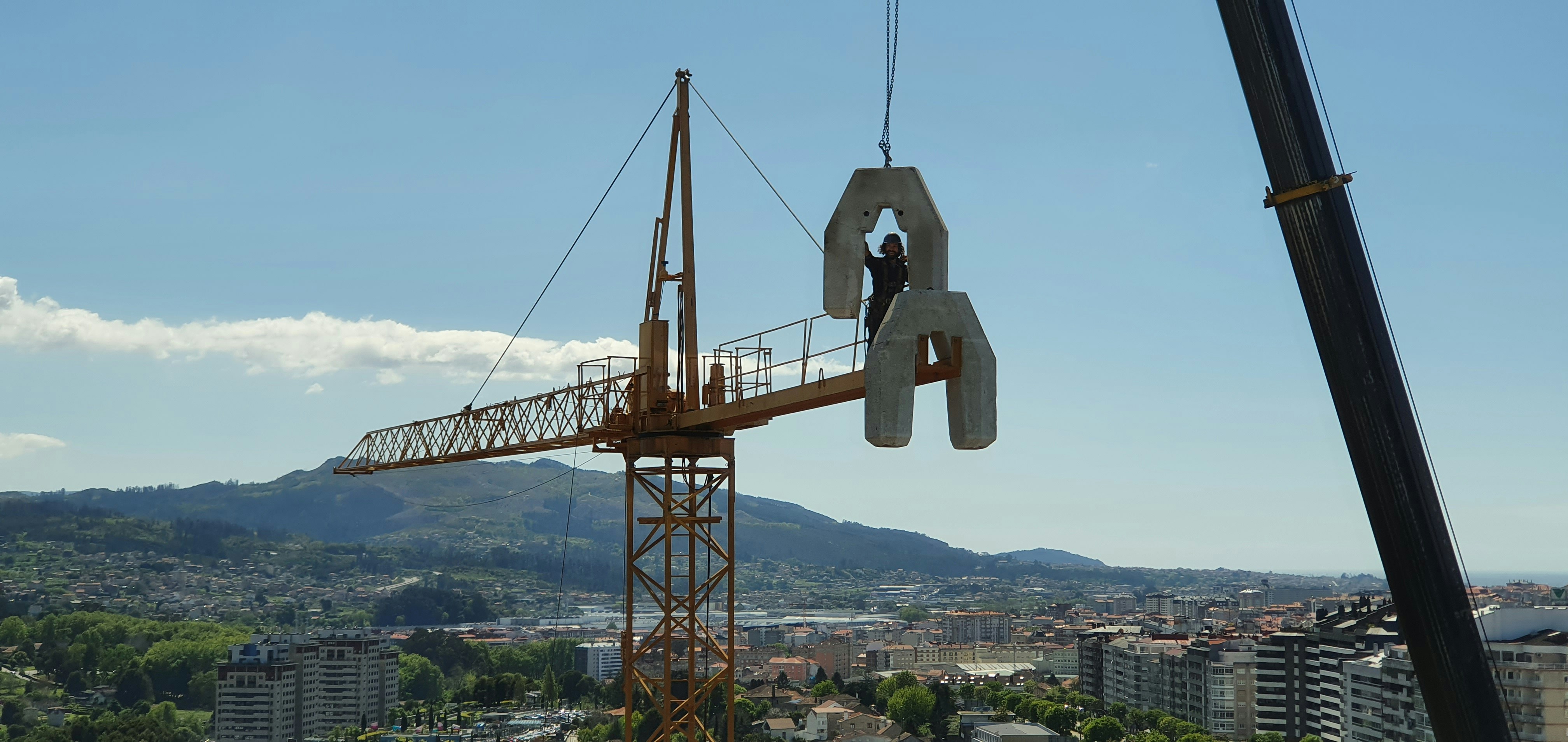 A smiling construction worker on the top of a really tall crane helping its assembly