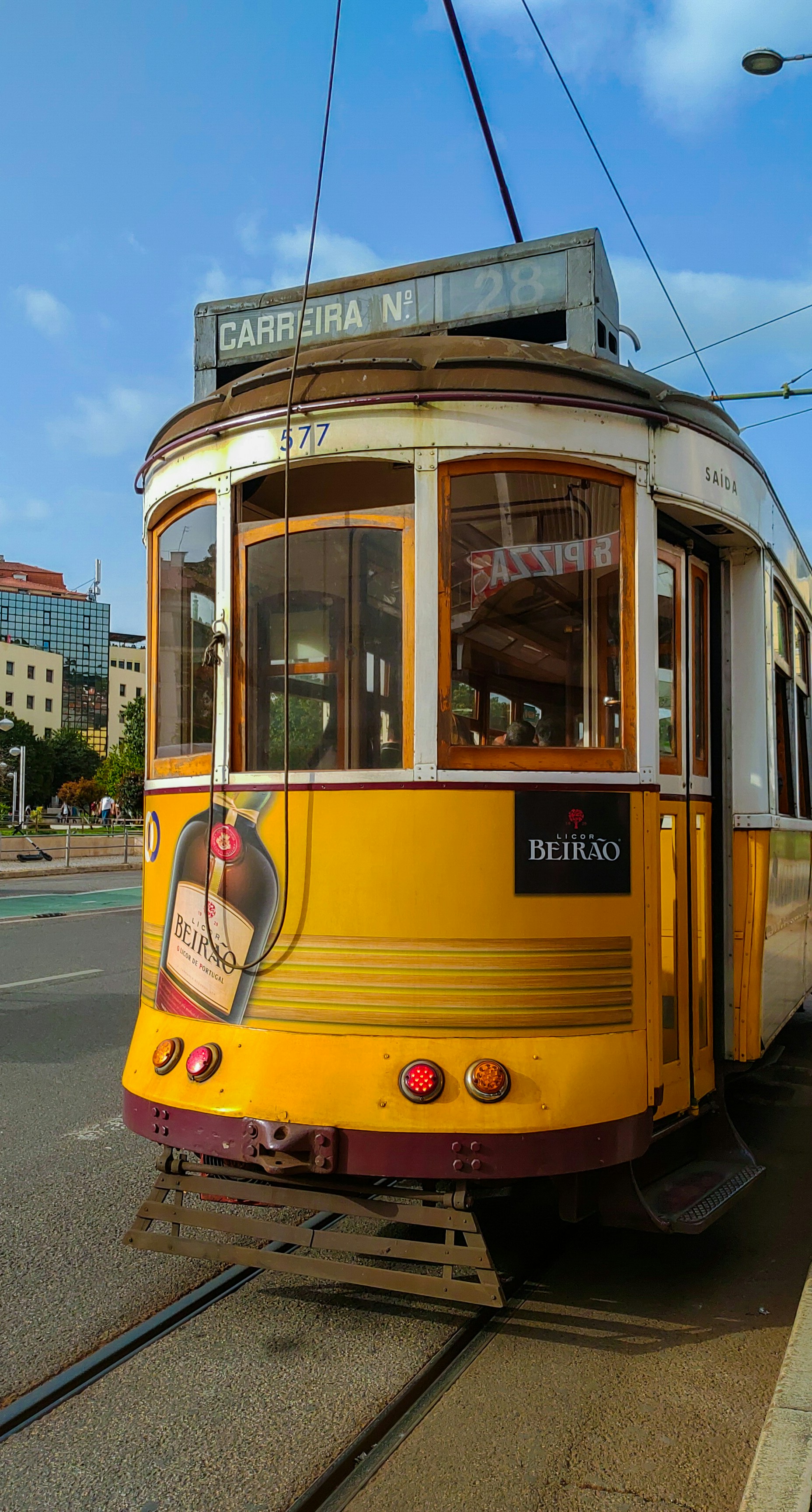 Photograph of a vintage yellow tram on tracks beside a city street against a blue sky.