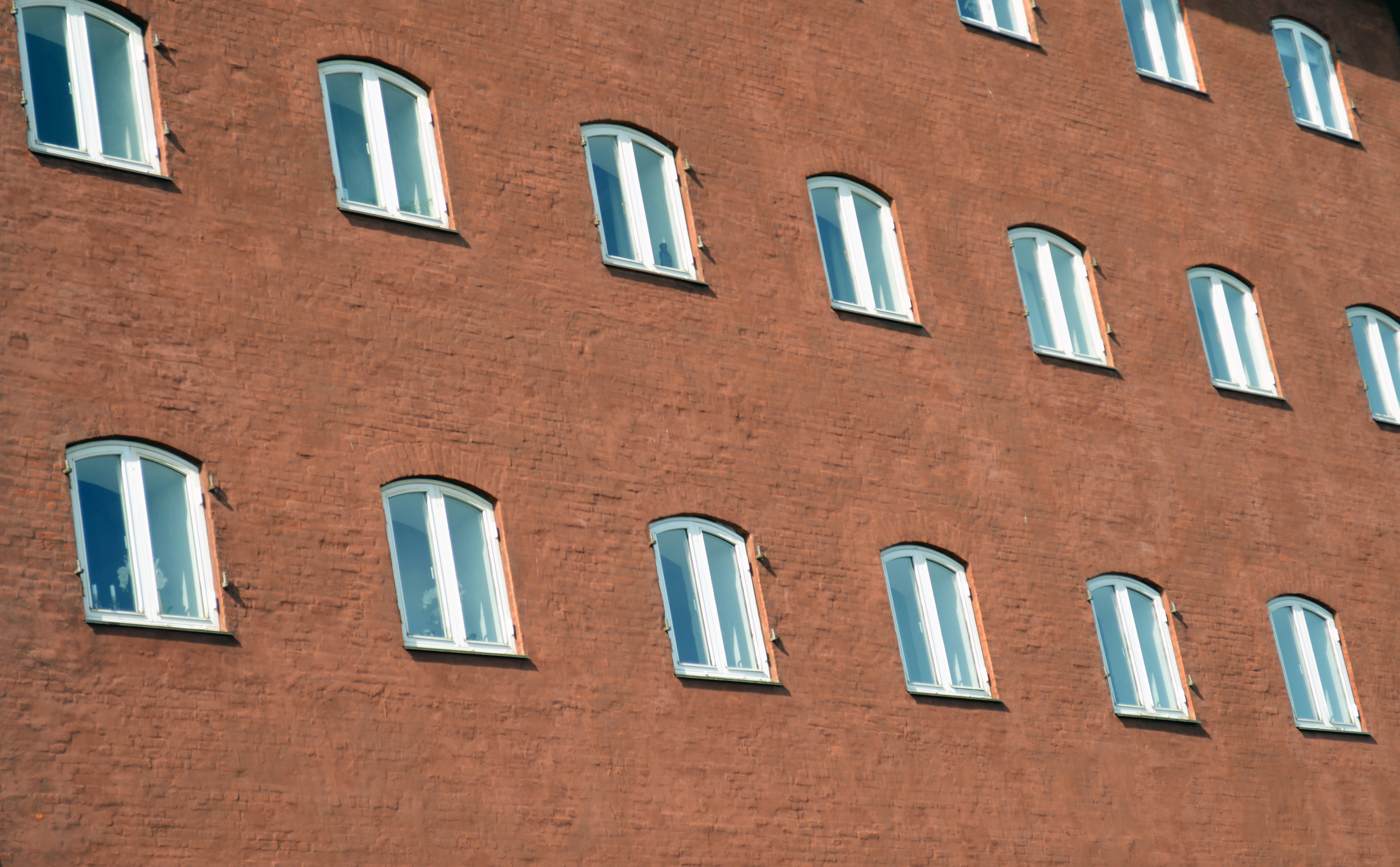 A close-up view of a brick wall adorned with a series of arched windows, reflecting light and the surrounding environment.