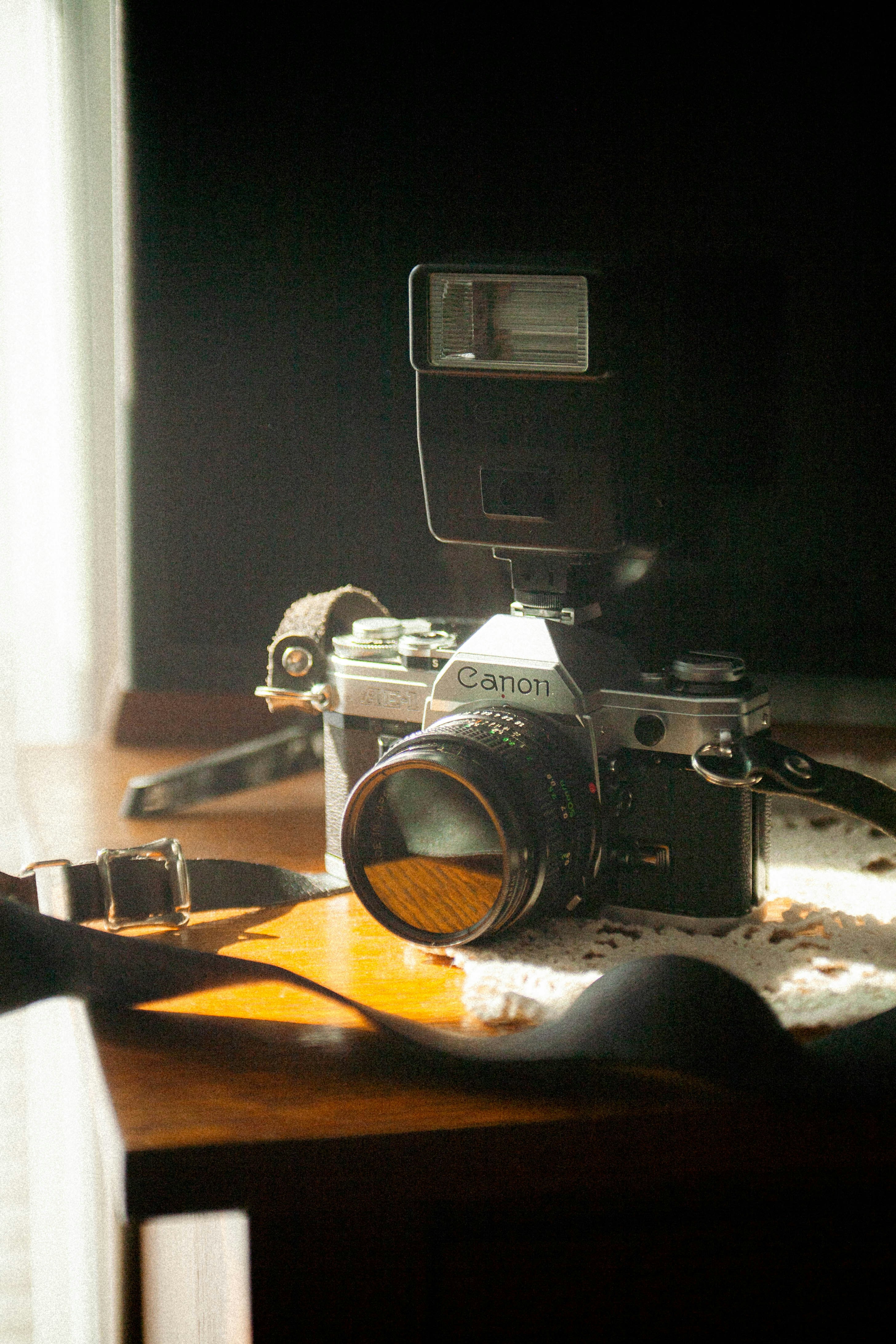 Vintage CANON camera with a flash unit resting on a wooden surface, illuminated by soft natural light.
