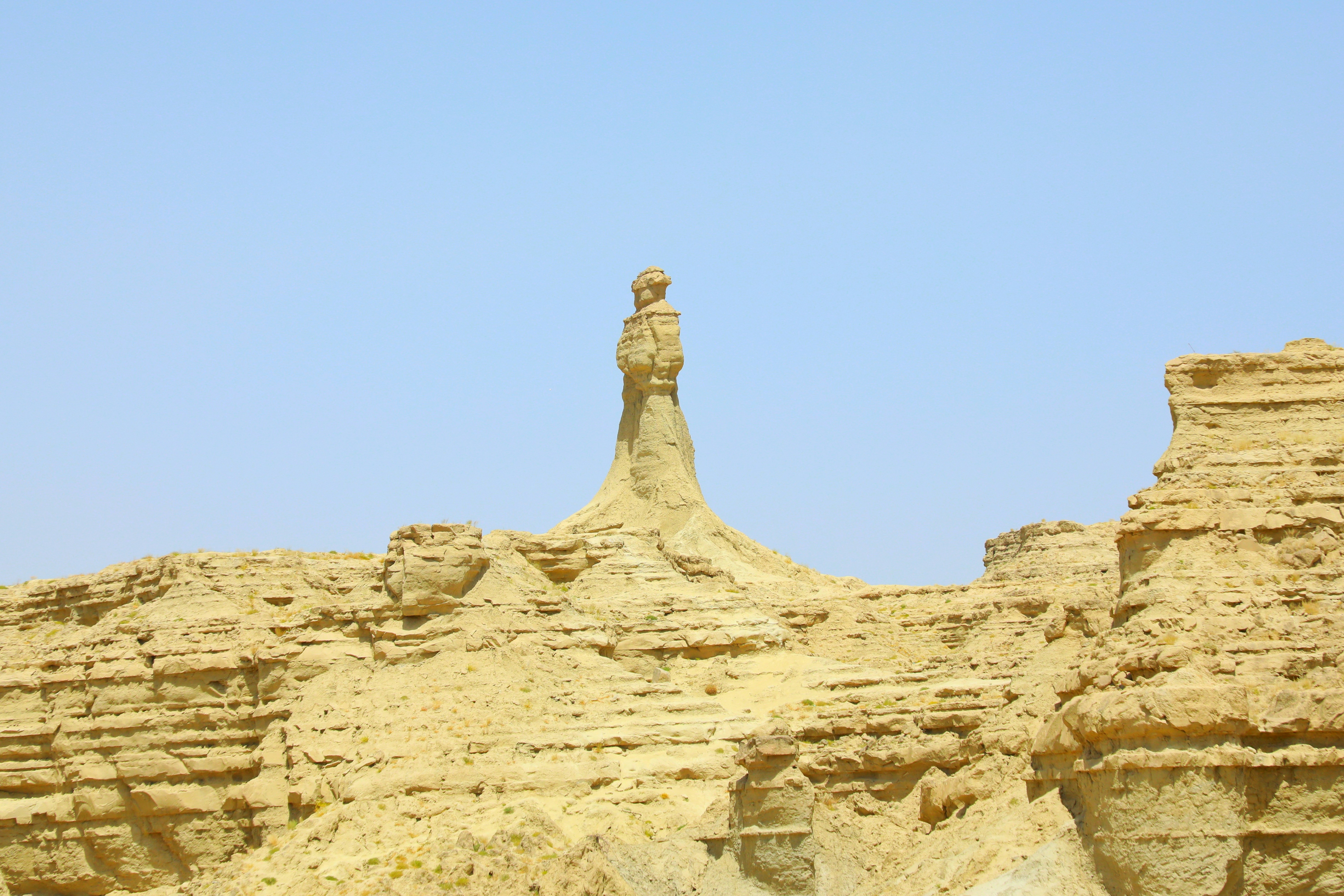 Natural rock formation resembling a solitary figure against a clear blue sky.