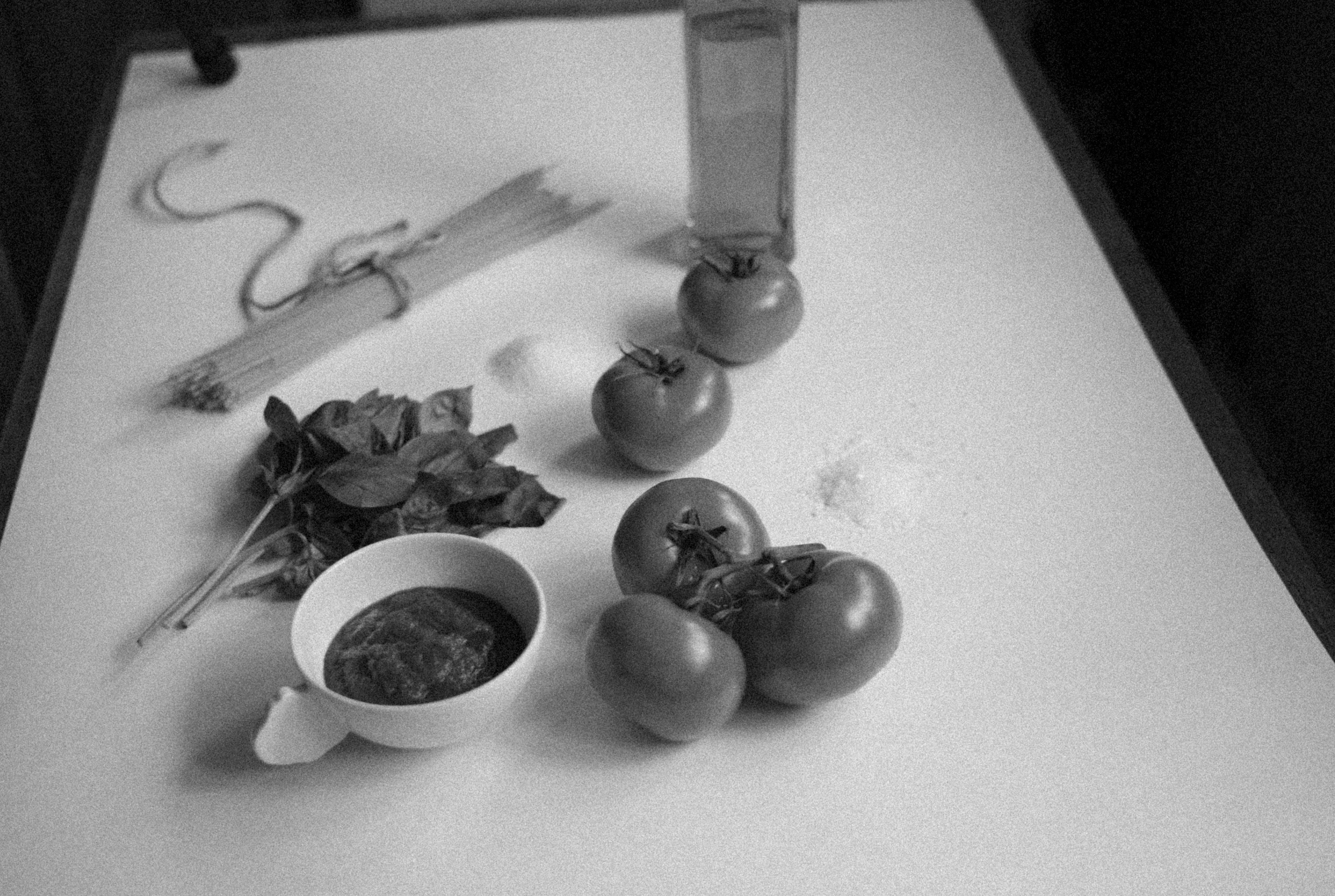 Arrangement of fresh tomatoes, herbs, and olive oil on a white surface, showcasing the ingredients for a delicious meal.