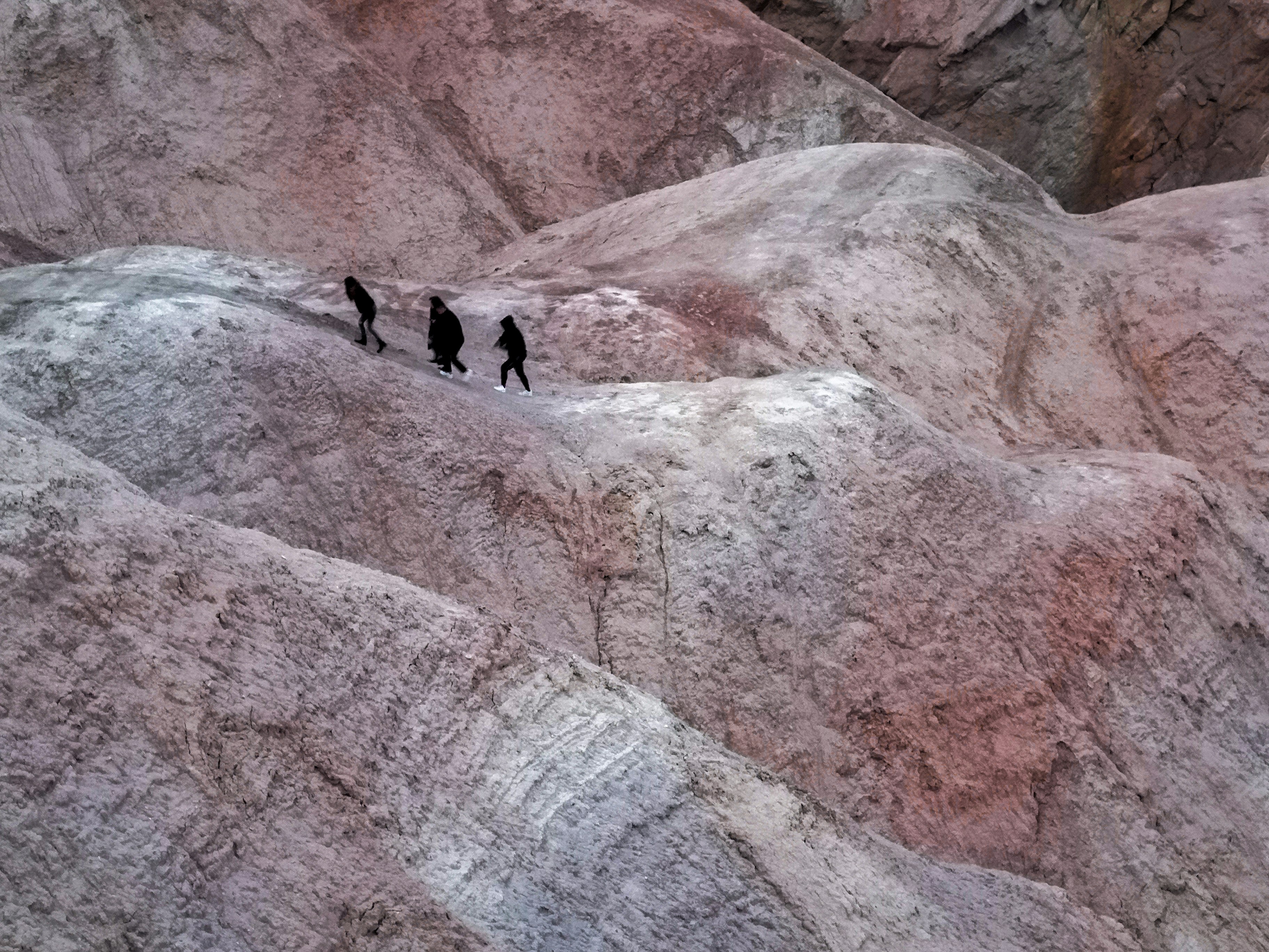 Silhouetted figures traverse a rugged, textured landscape, illuminated by soft hues of dusk.