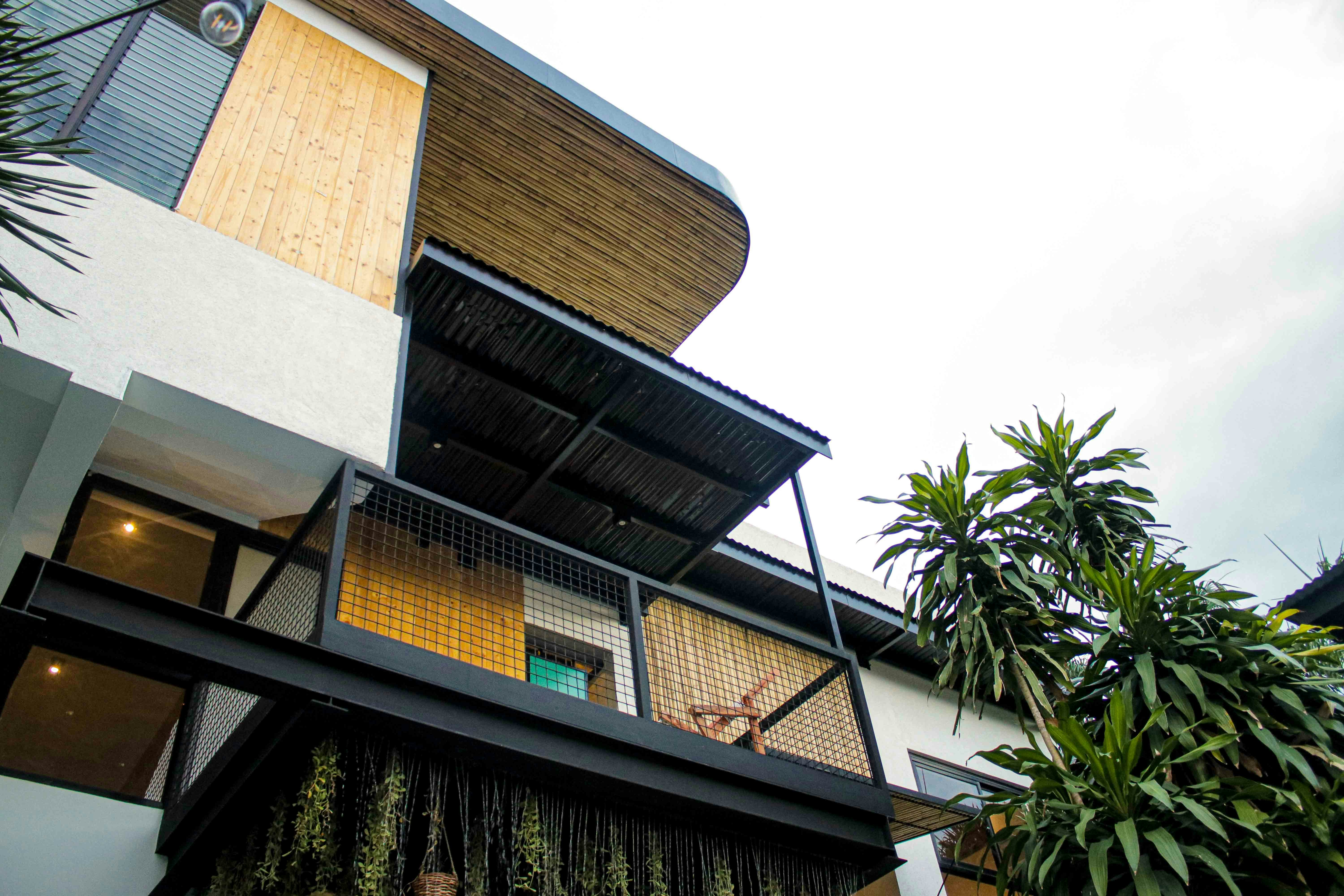 Contemporary house design featuring a blend of wood and metal elements, surrounded by lush greenery and a clear sky.