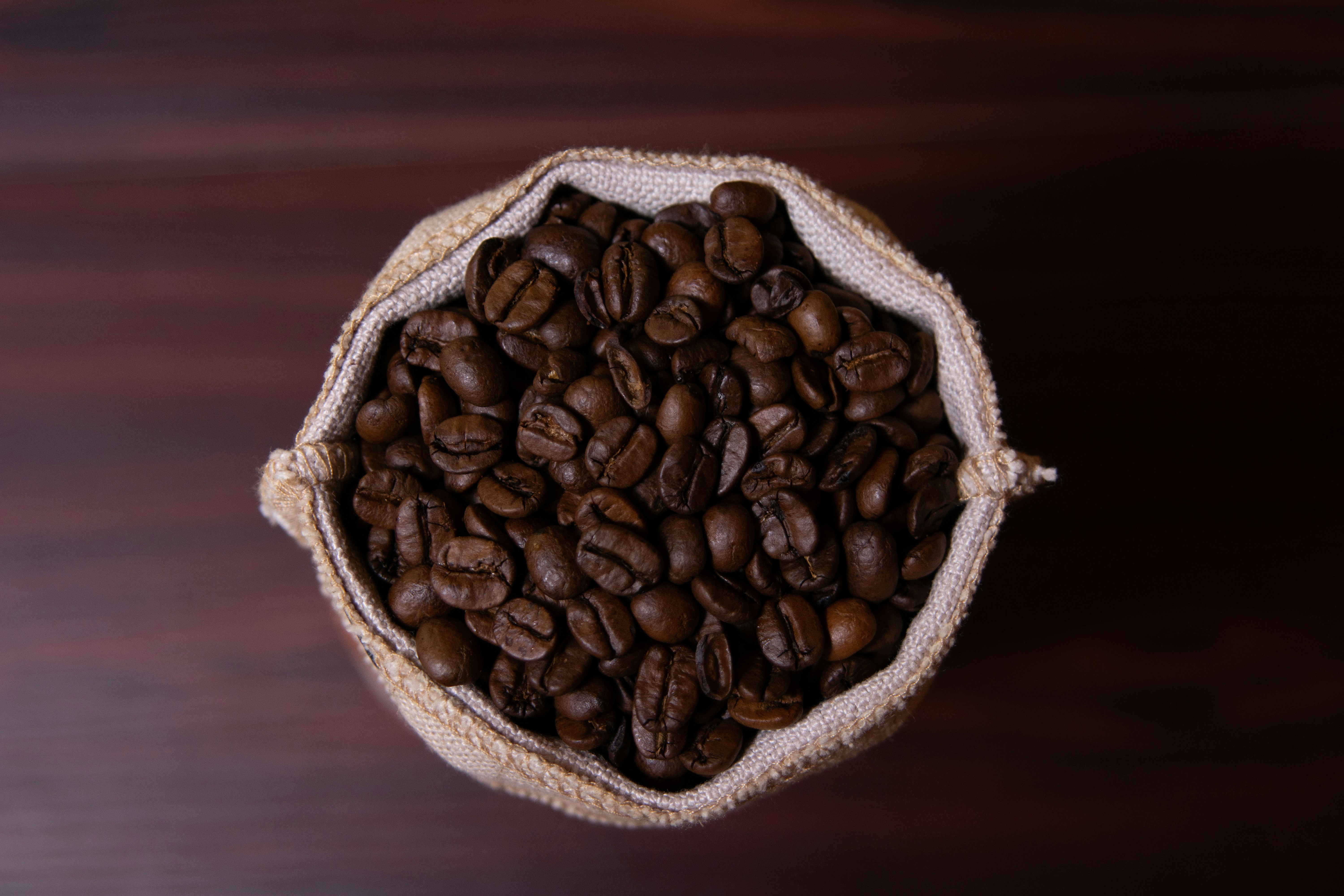 Close-up of a burlap sack filled with roasted coffee beans, showcasing their rich texture and color. The composition highlights the natural beauty of the beans.