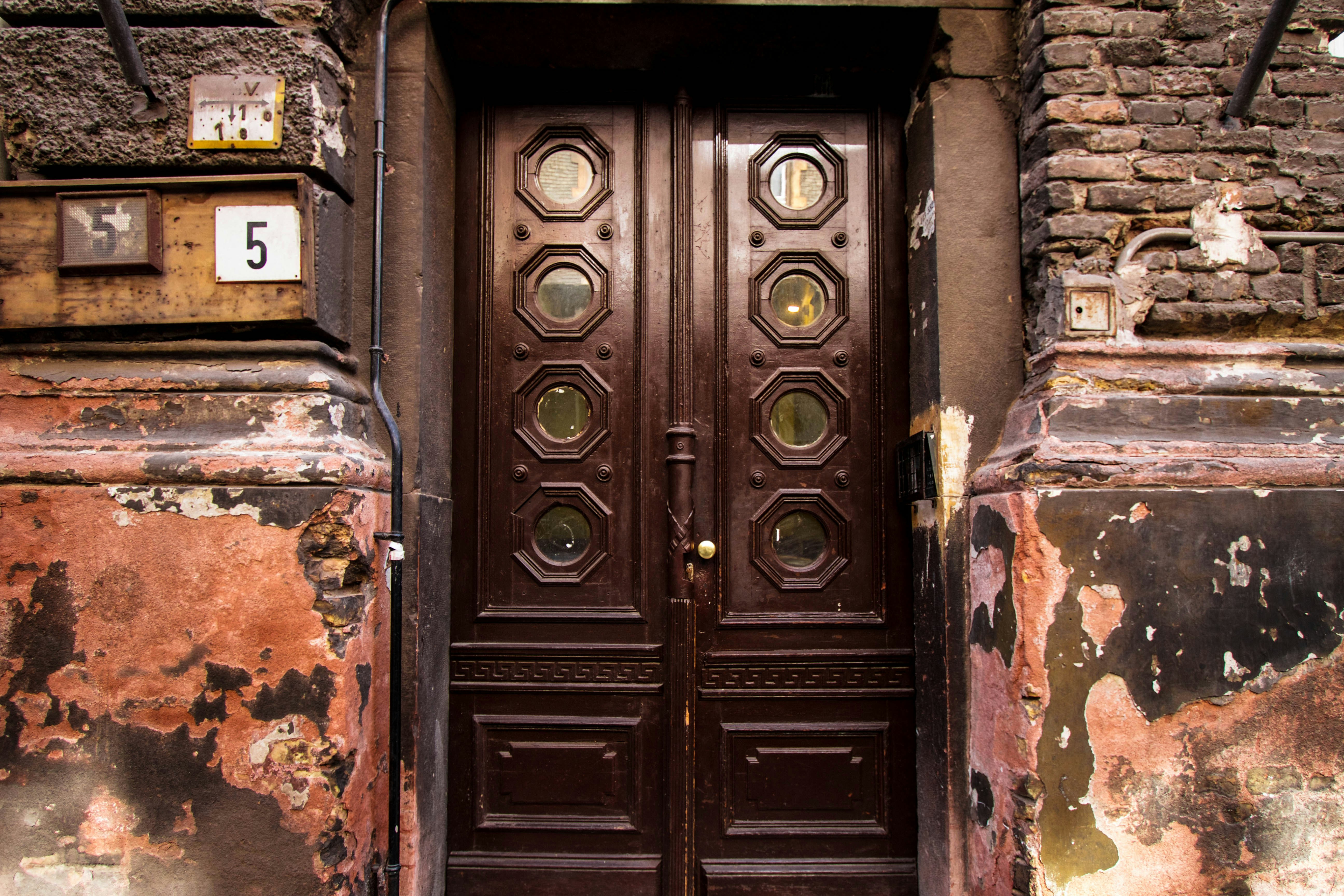 Intricately designed wooden doors with octagonal glass panels stand against a backdrop of peeling paint and weathered bricks.