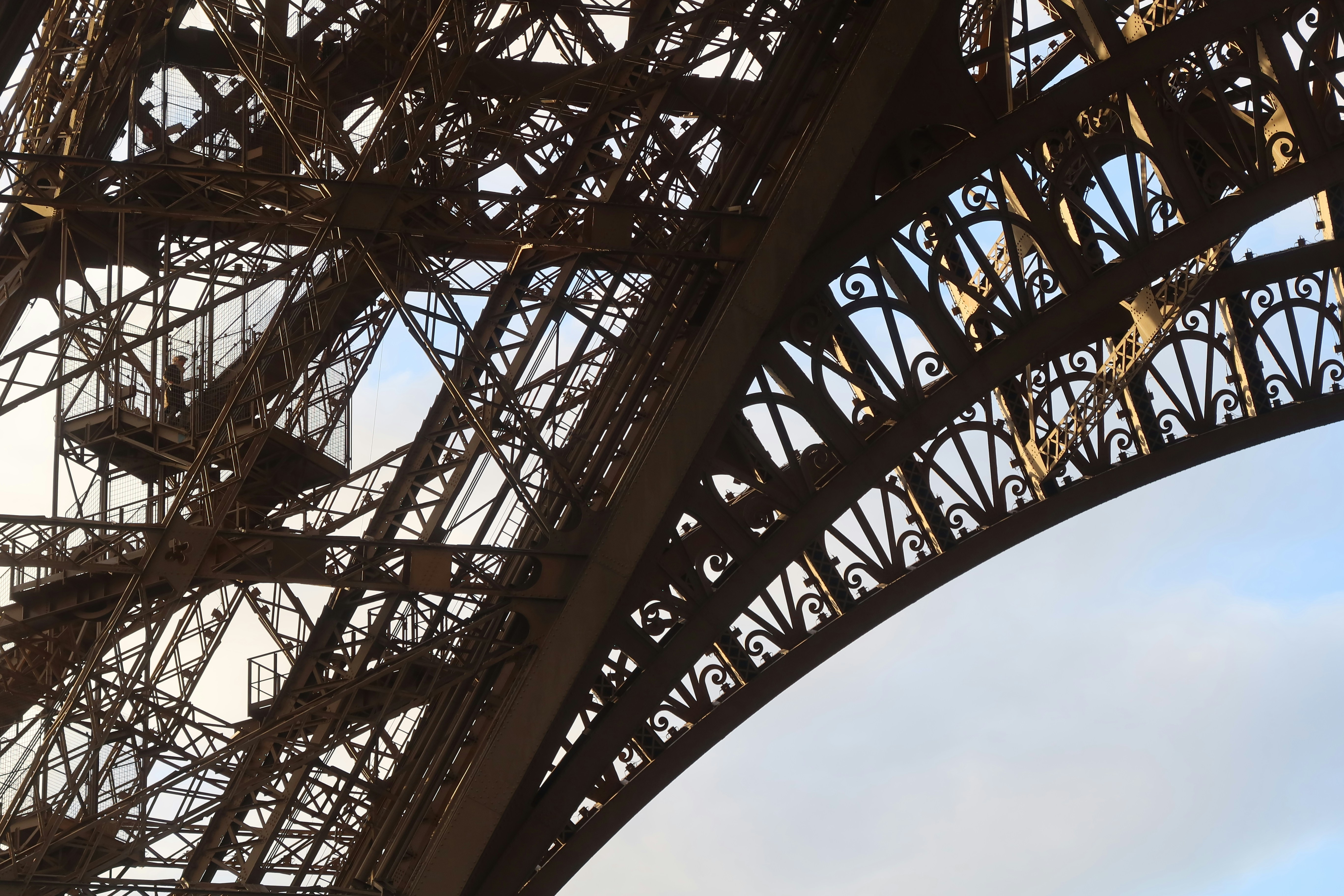 Detailed view of the intricate iron lattice of the Eiffel Tower, showcasing its architectural elegance against a cloudy sky.