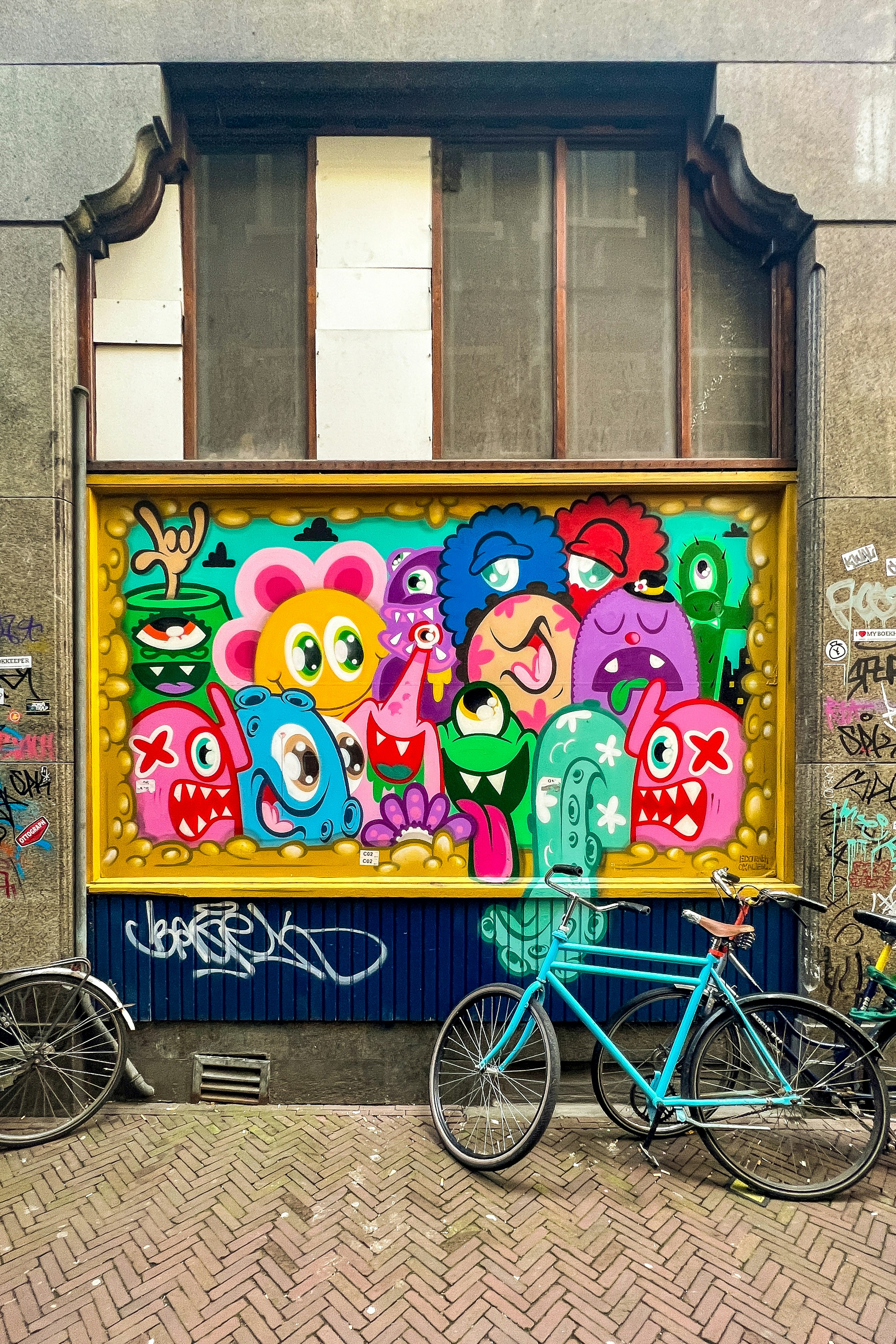 Colorful mural of playful monsters framed by a golden border with bicycles resting outside