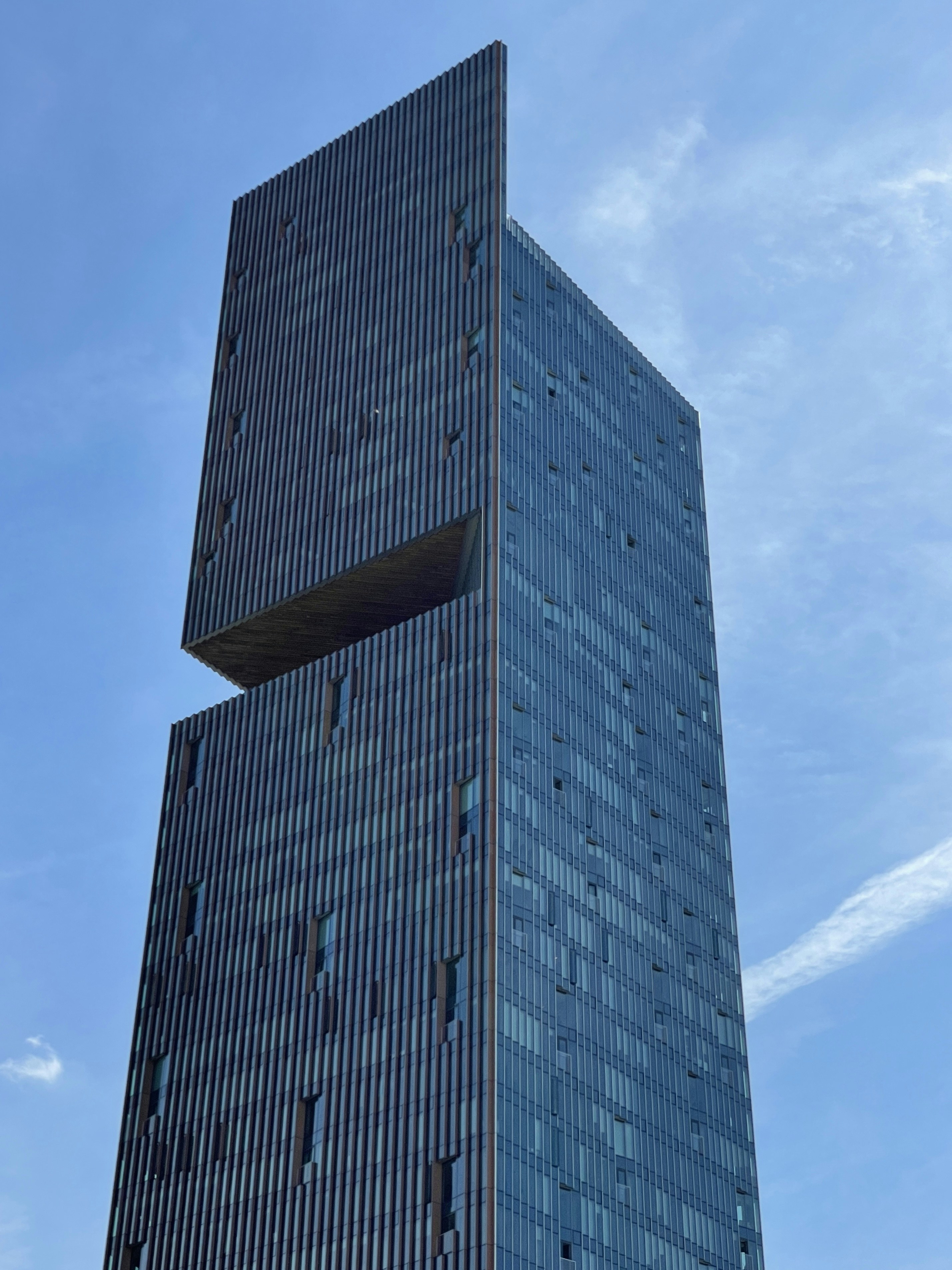 A modern skyscraper featuring a striking cantilever design and reflective glass facade against a clear blue sky.